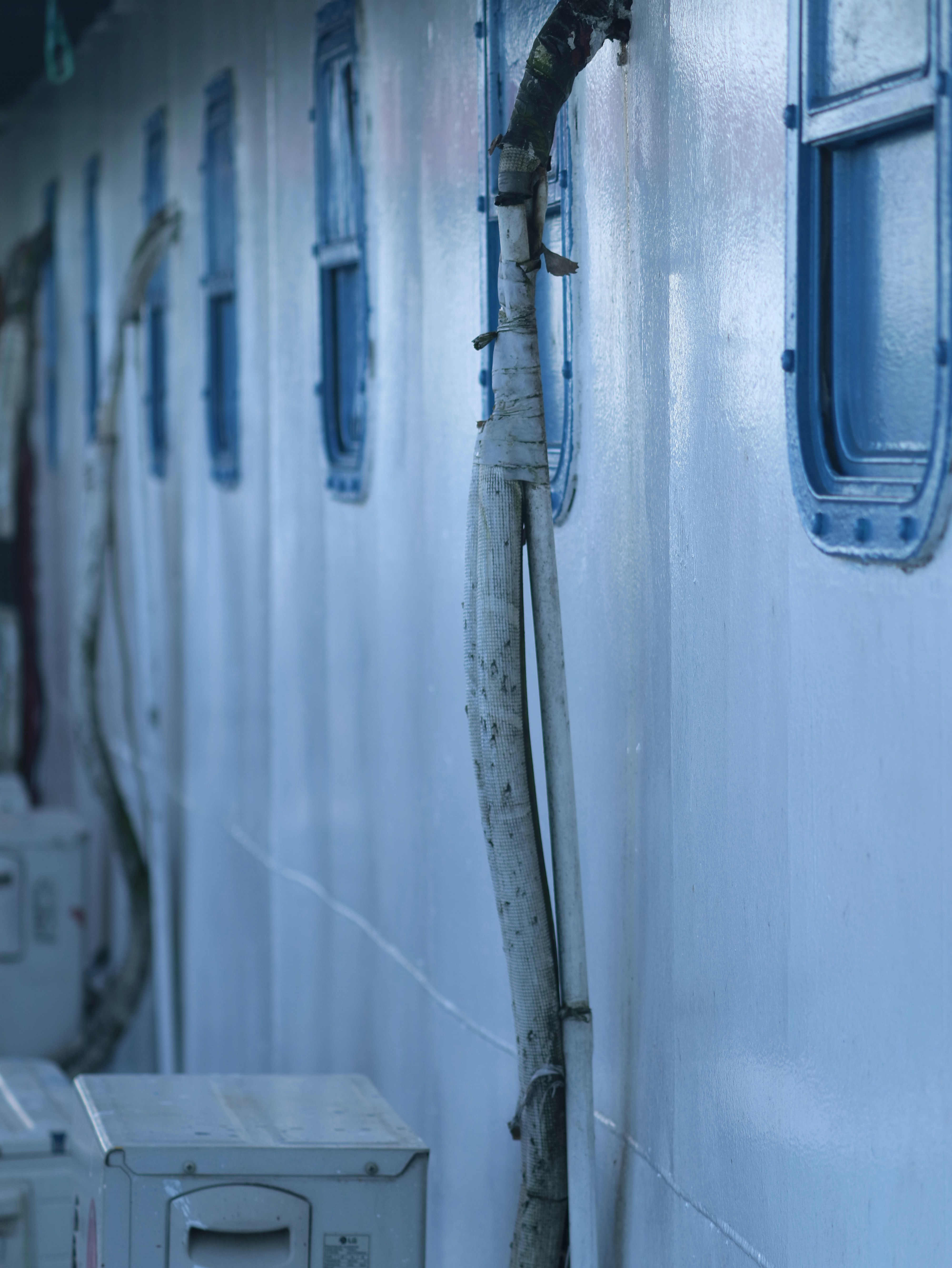 Close-up of a textured blue wall on a ship, featuring windows and electrical conduits, evoking a sense of maritime industry.