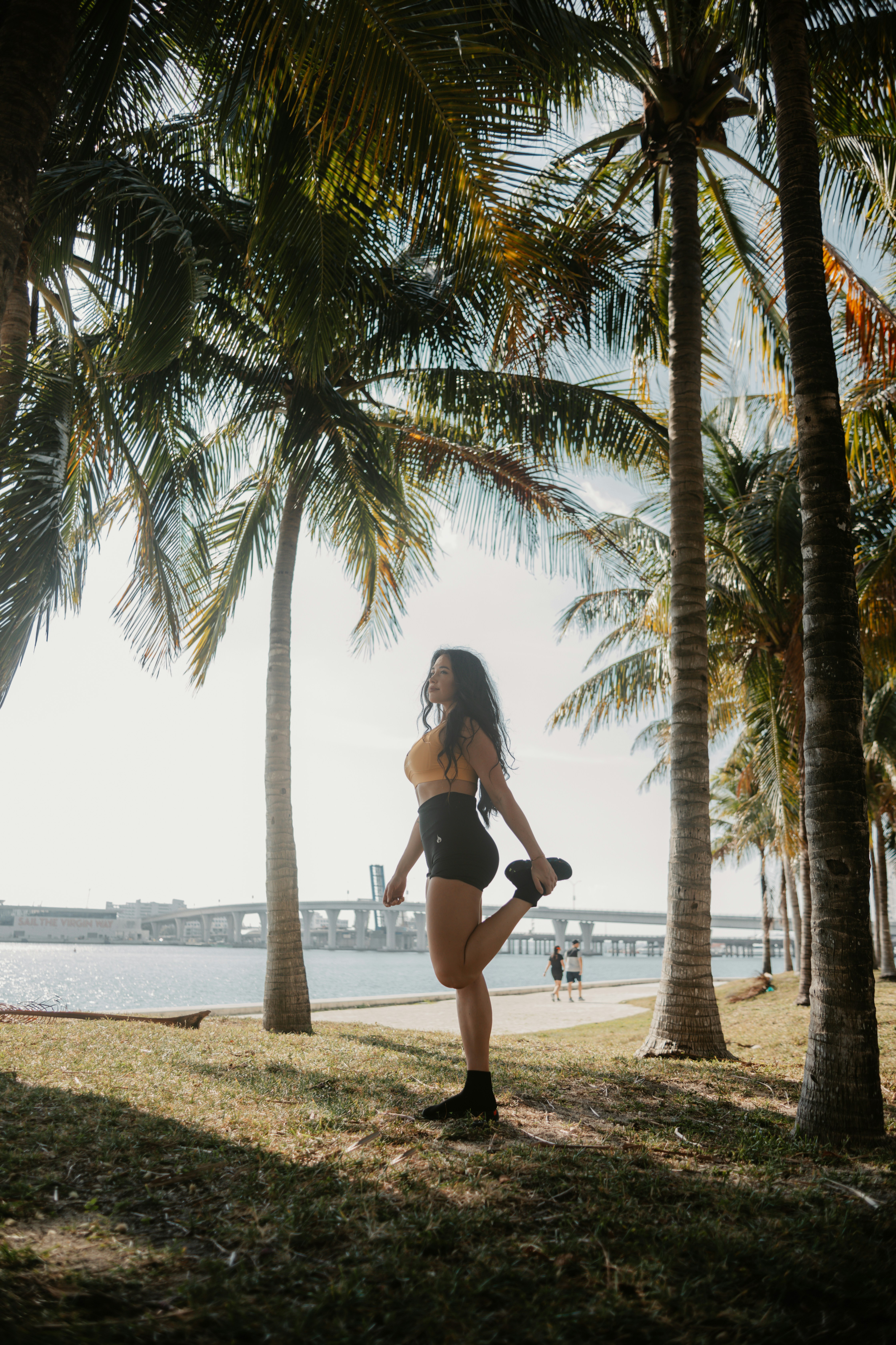 A woman stretching by the waterfront under swaying palm trees, exuding a sense of calm and vitality.