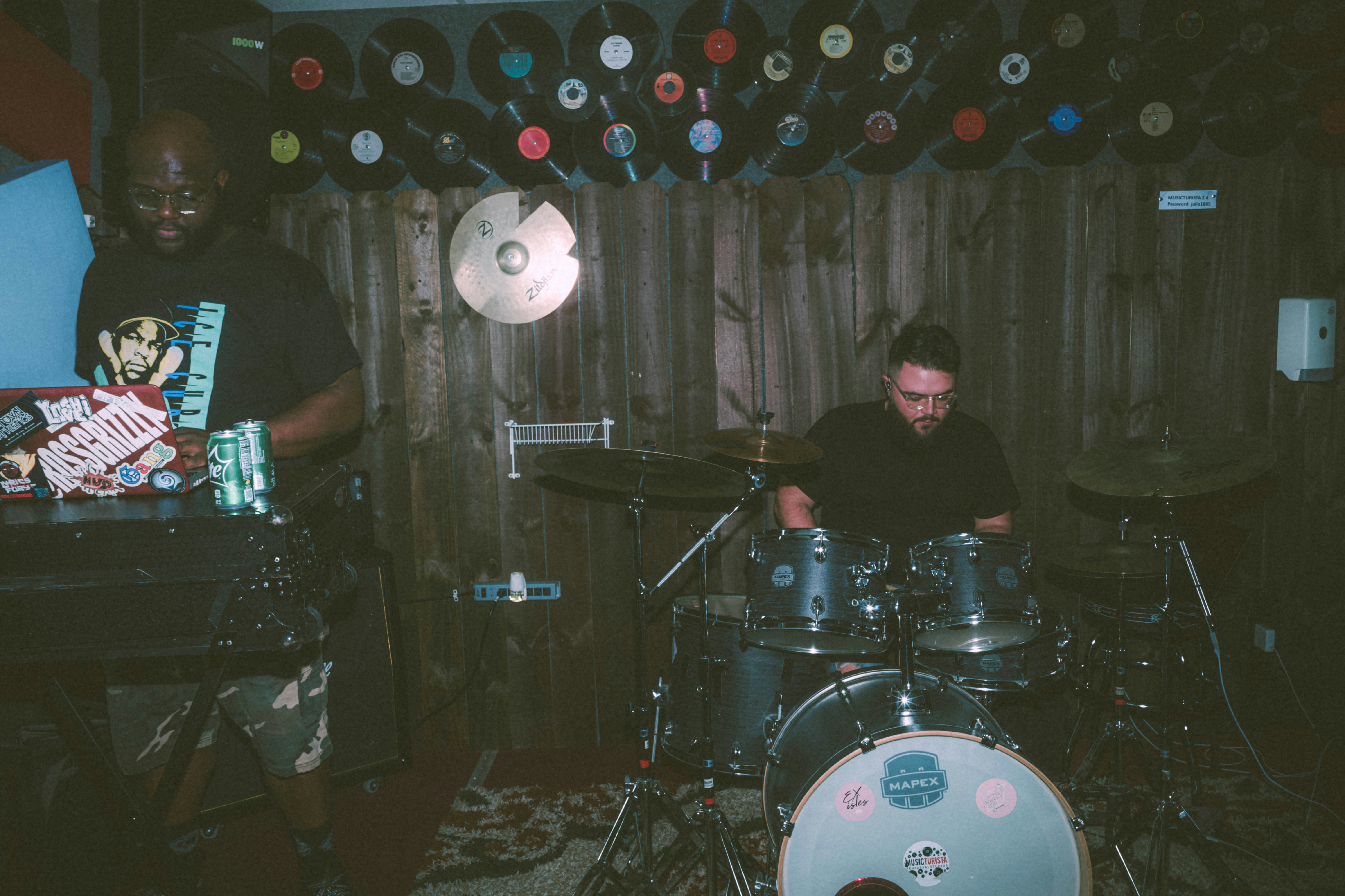 Two musicians perform in a cozy venue adorned with vinyl records. The energy of the moment is palpable as they create music together.