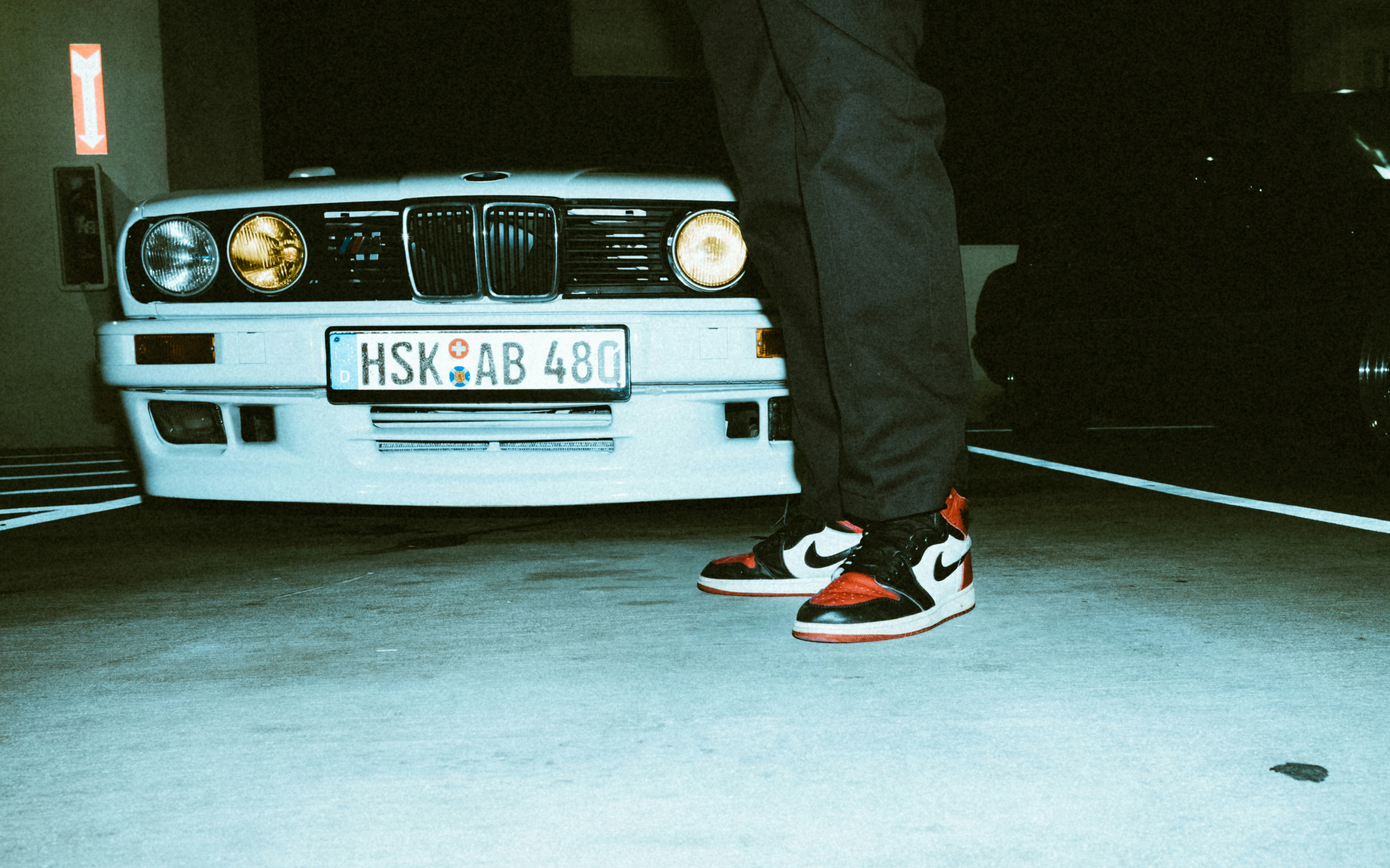 A pair of stylish sneakers in front of a vintage white BMW, highlighting the intersection of modern fashion and classic automotive design.