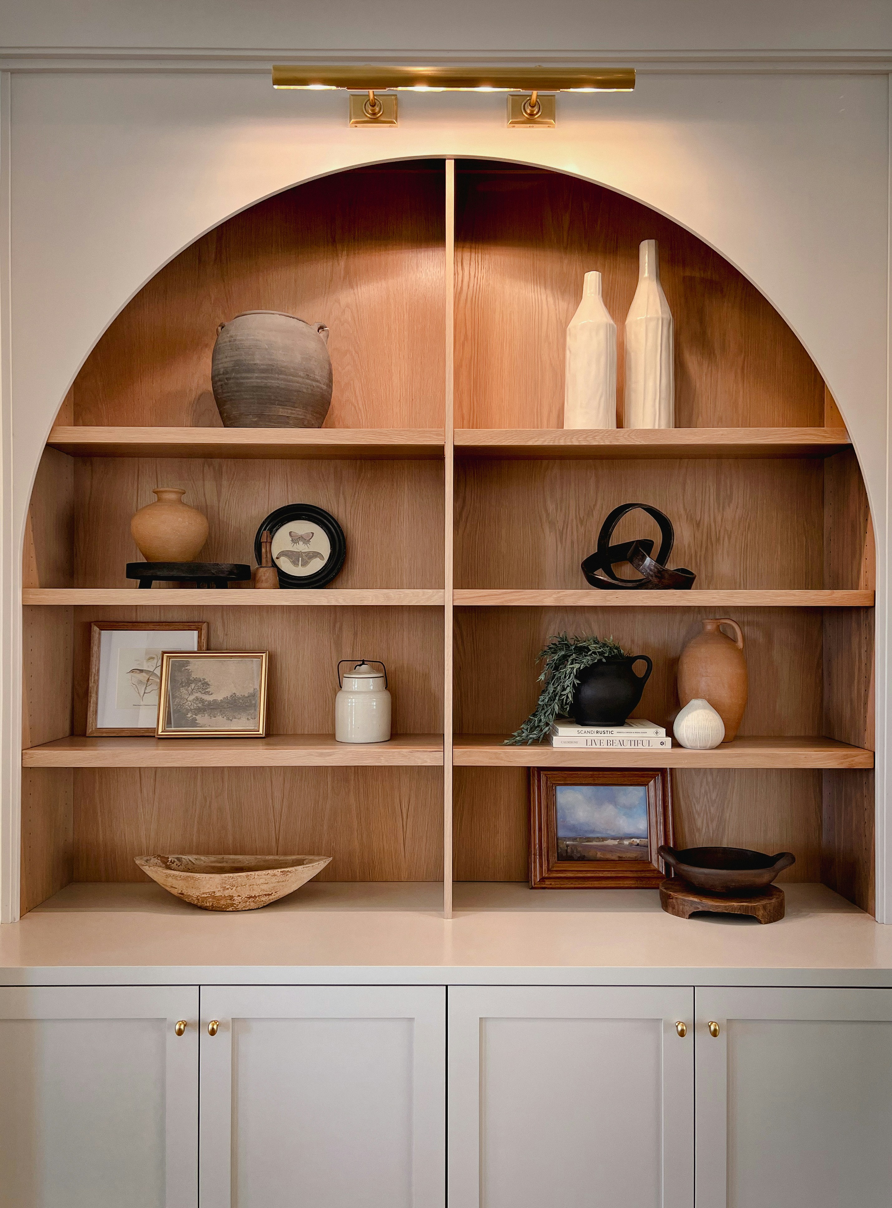 Stylish wooden shelving displaying an assortment of pottery, framed art, and decorative items, highlighted by soft lighting.