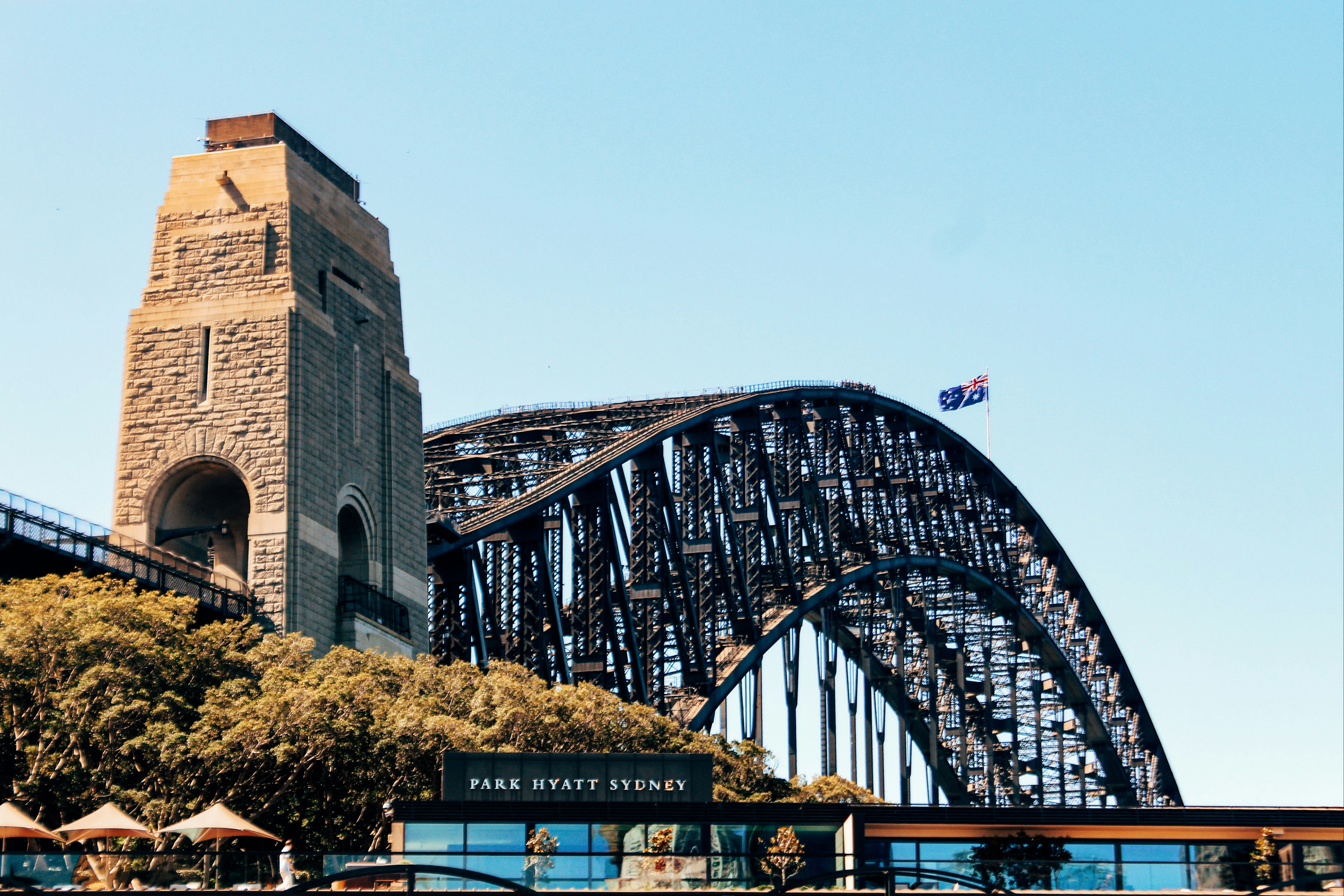 Sydney Harbour Bridge arches above the Park Hyatt with clear blue skies and an Australian flag waving.