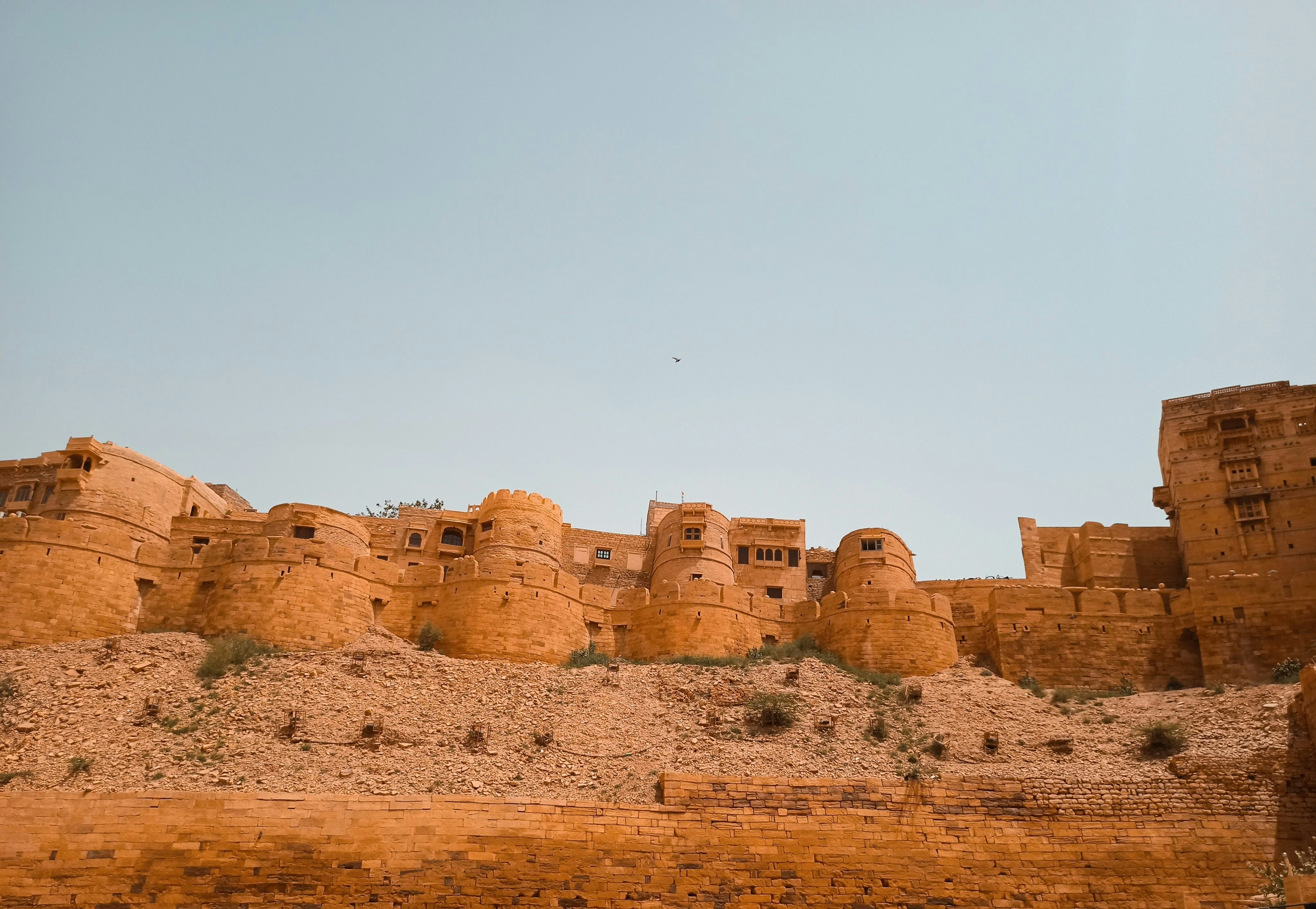 Ancient sandstone fortification rising against a clear sky, showcasing intricate architectural details and a rugged landscape.