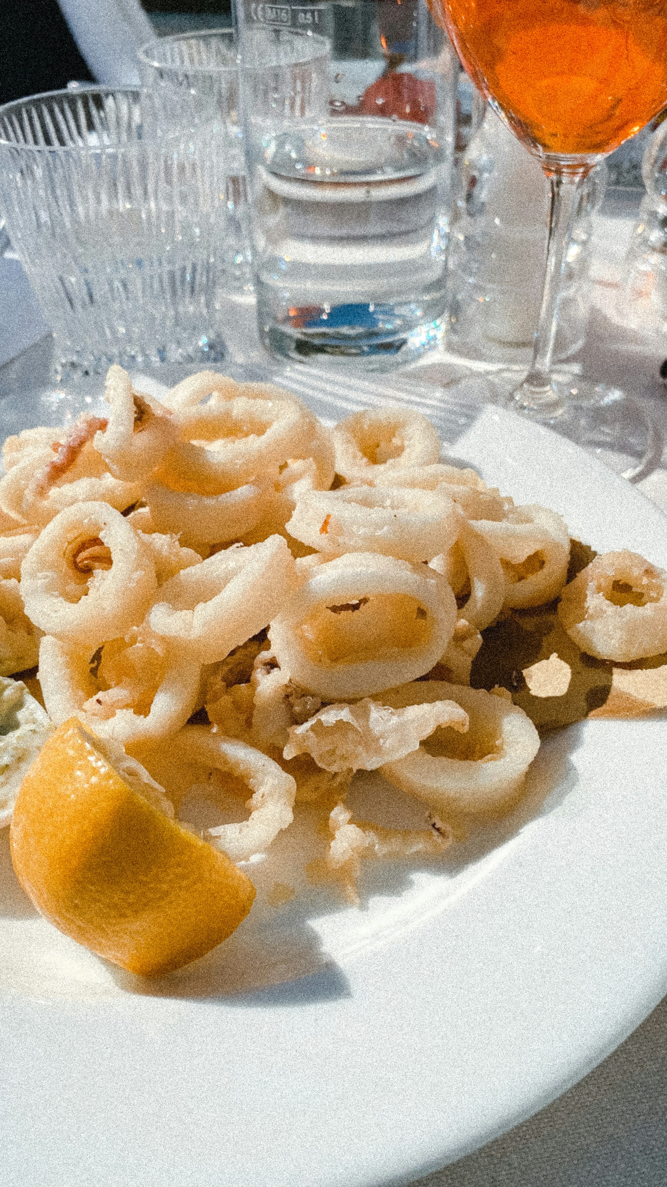 Plate of crispy calamari rings garnished with a lemon wedge, accompanied by a refreshing drink in the background.