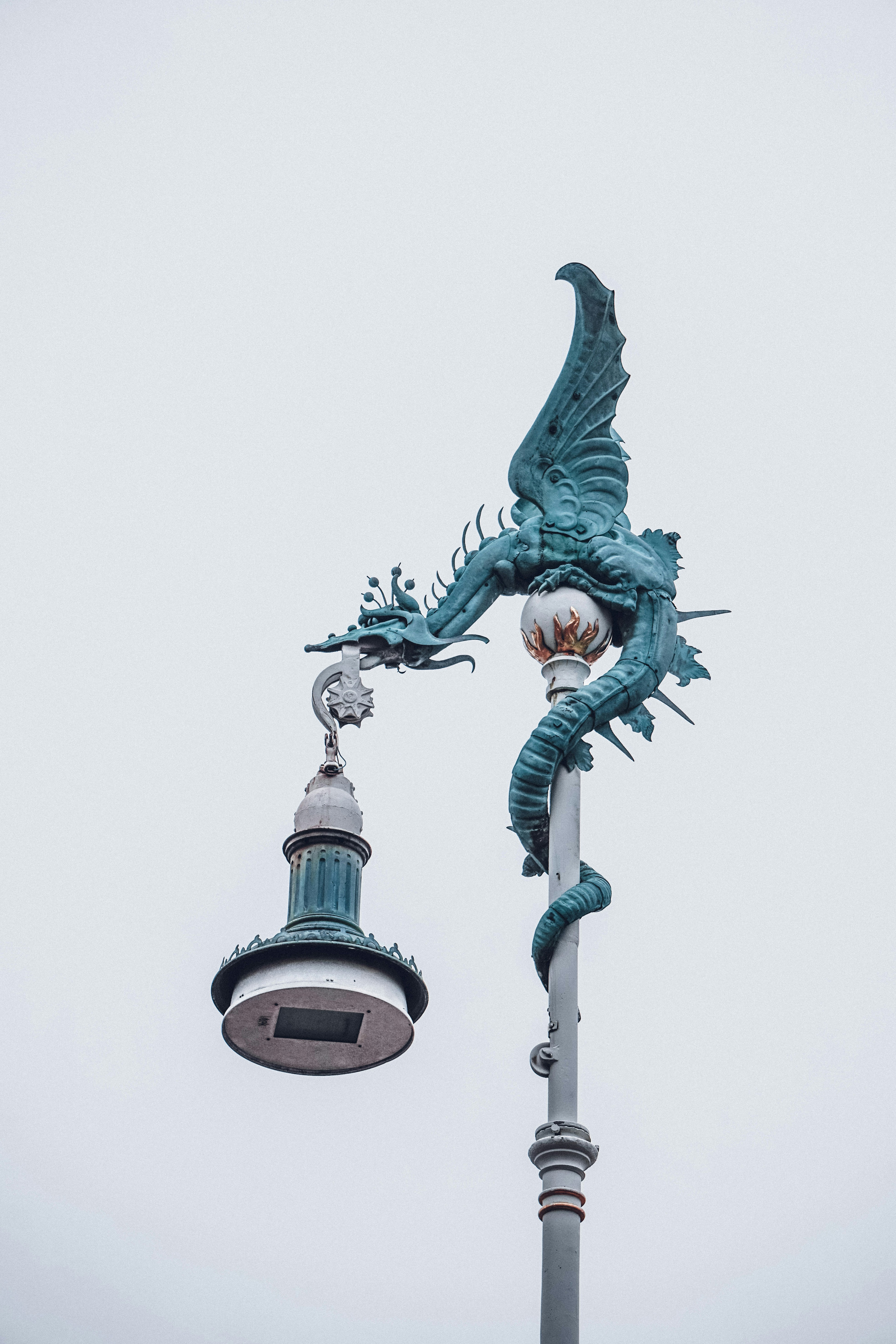 Ornate dragon-shaped lamp post featuring a bell-shaped lantern, set against a gray sky.