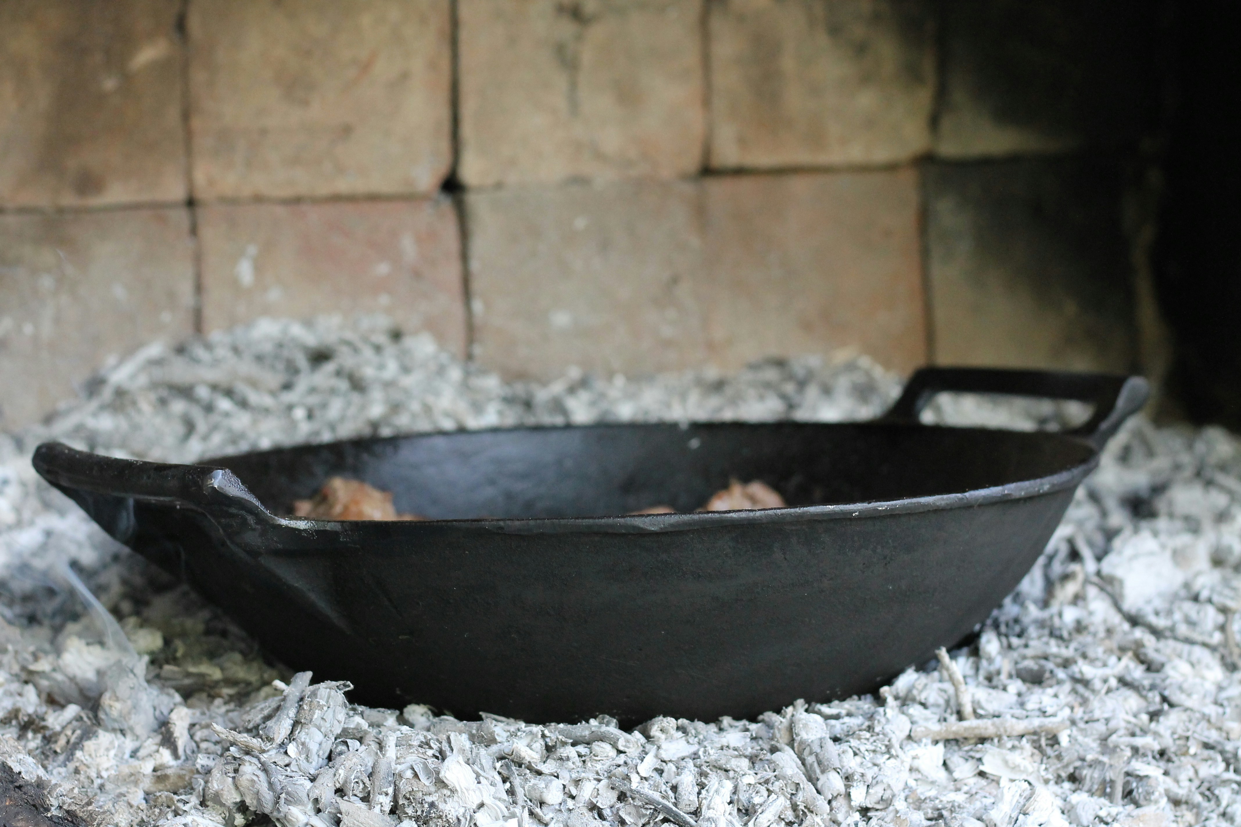 Cast iron pan resting in a bed of ash, showcasing the rustic charm of traditional cooking methods. The textured surface hints at culinary stories of the past.