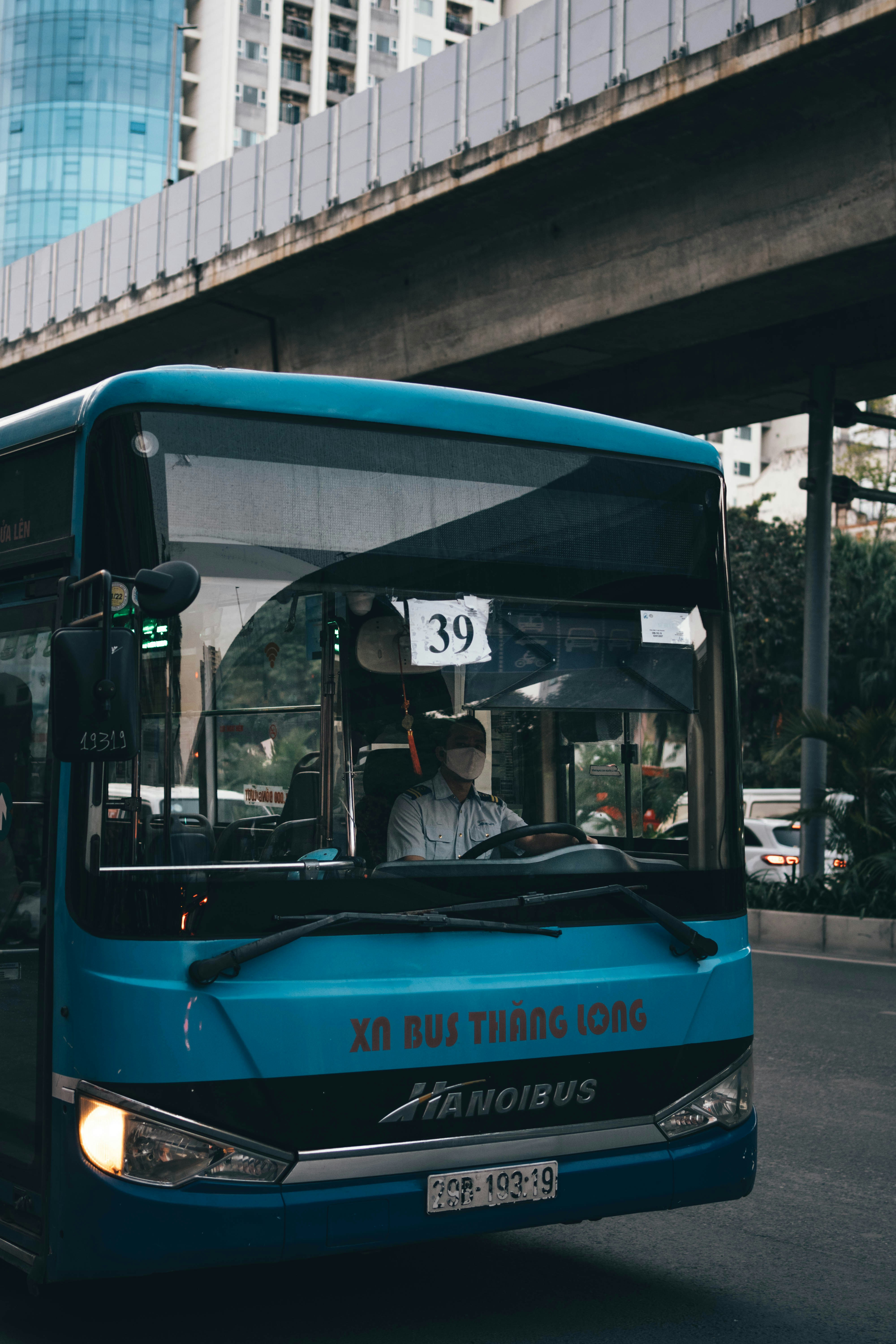 a blue bus driving down a street next to a bridge