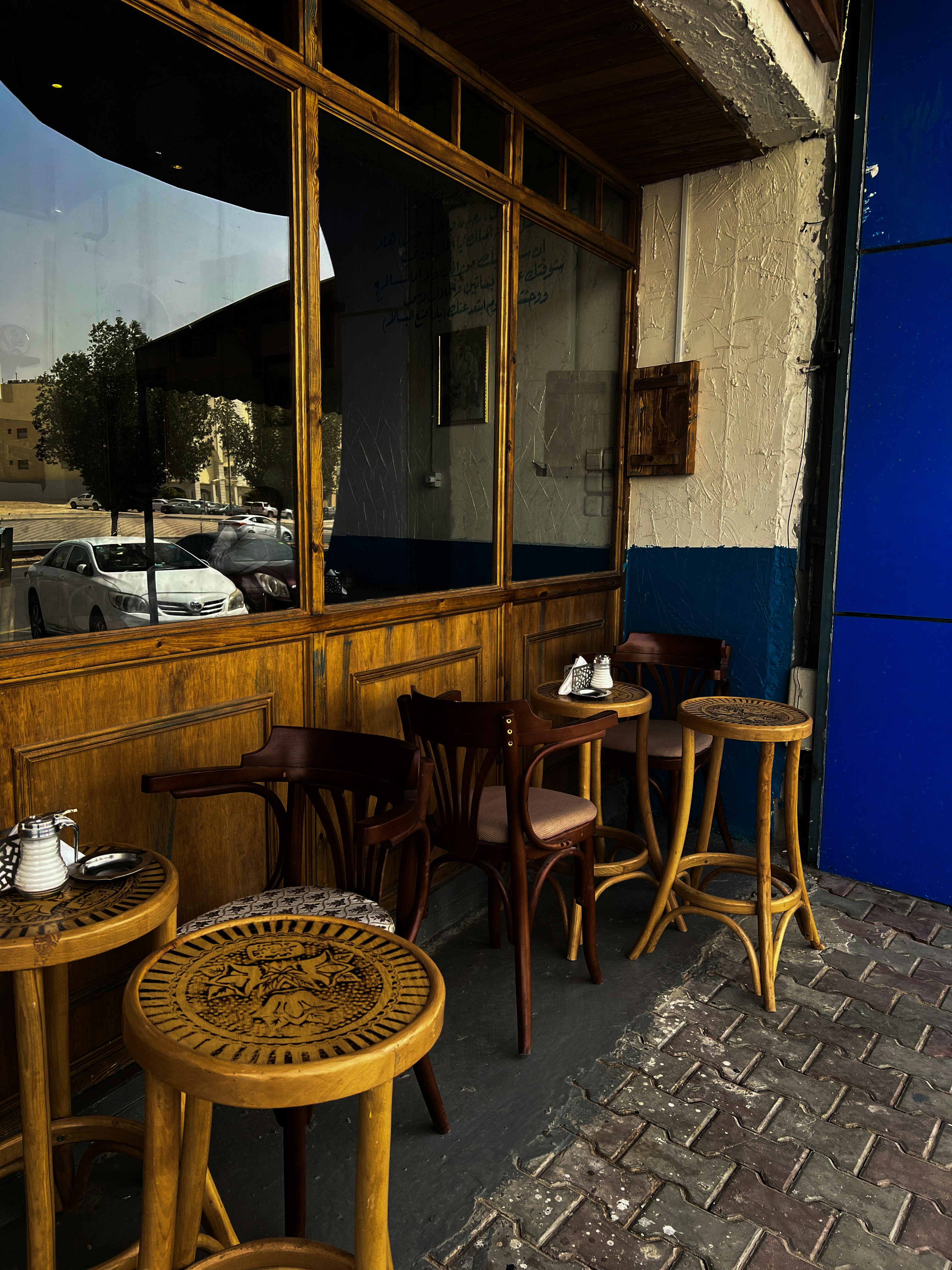 Cozy café seating arrangement featuring intricately designed wooden tables and chairs, with reflections of the outside world visible in large windows.