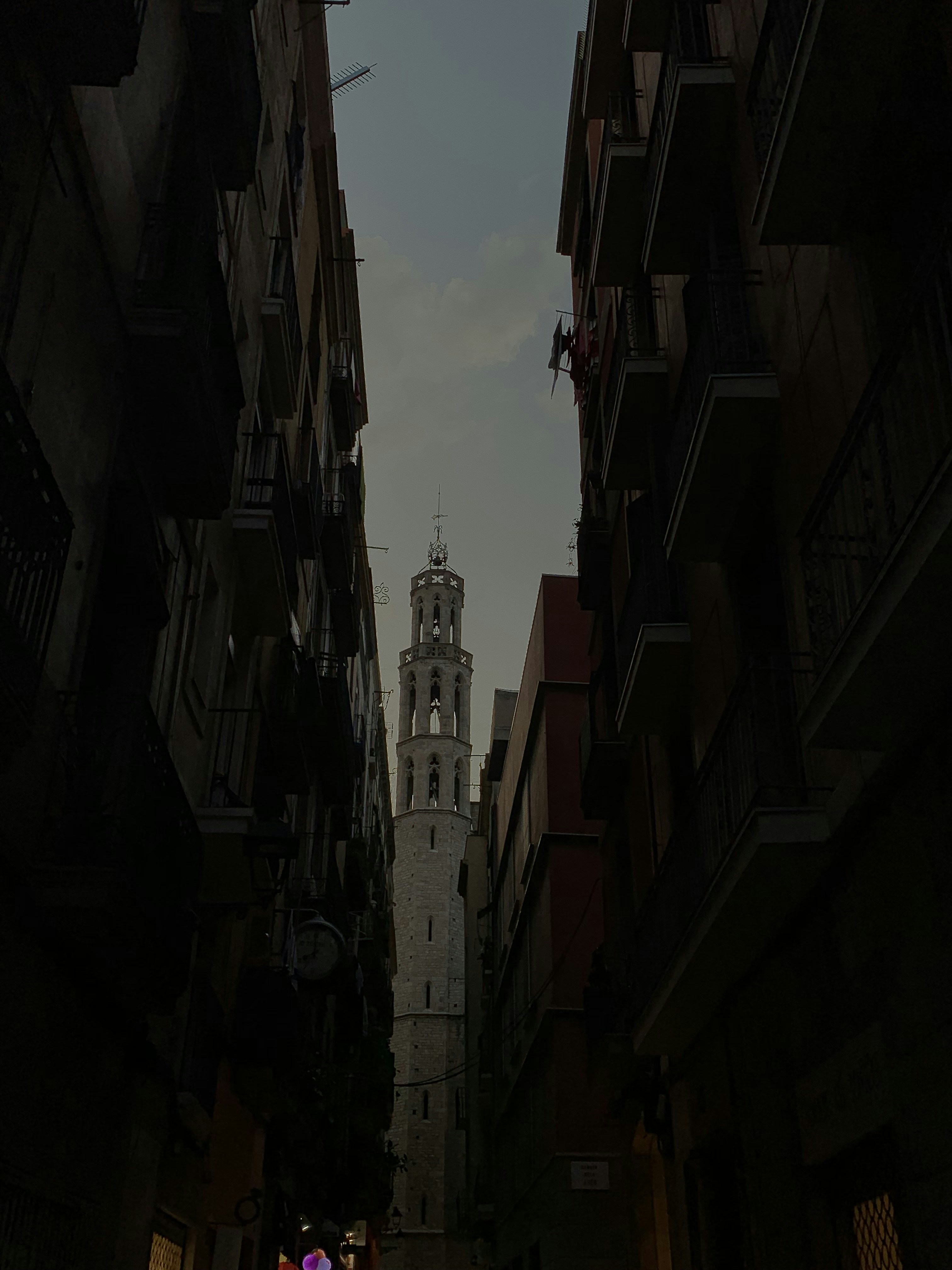 Historic tower rises above narrow alleyway, framed by buildings in twilight. The scene captures a blend of architectural beauty and urban life.