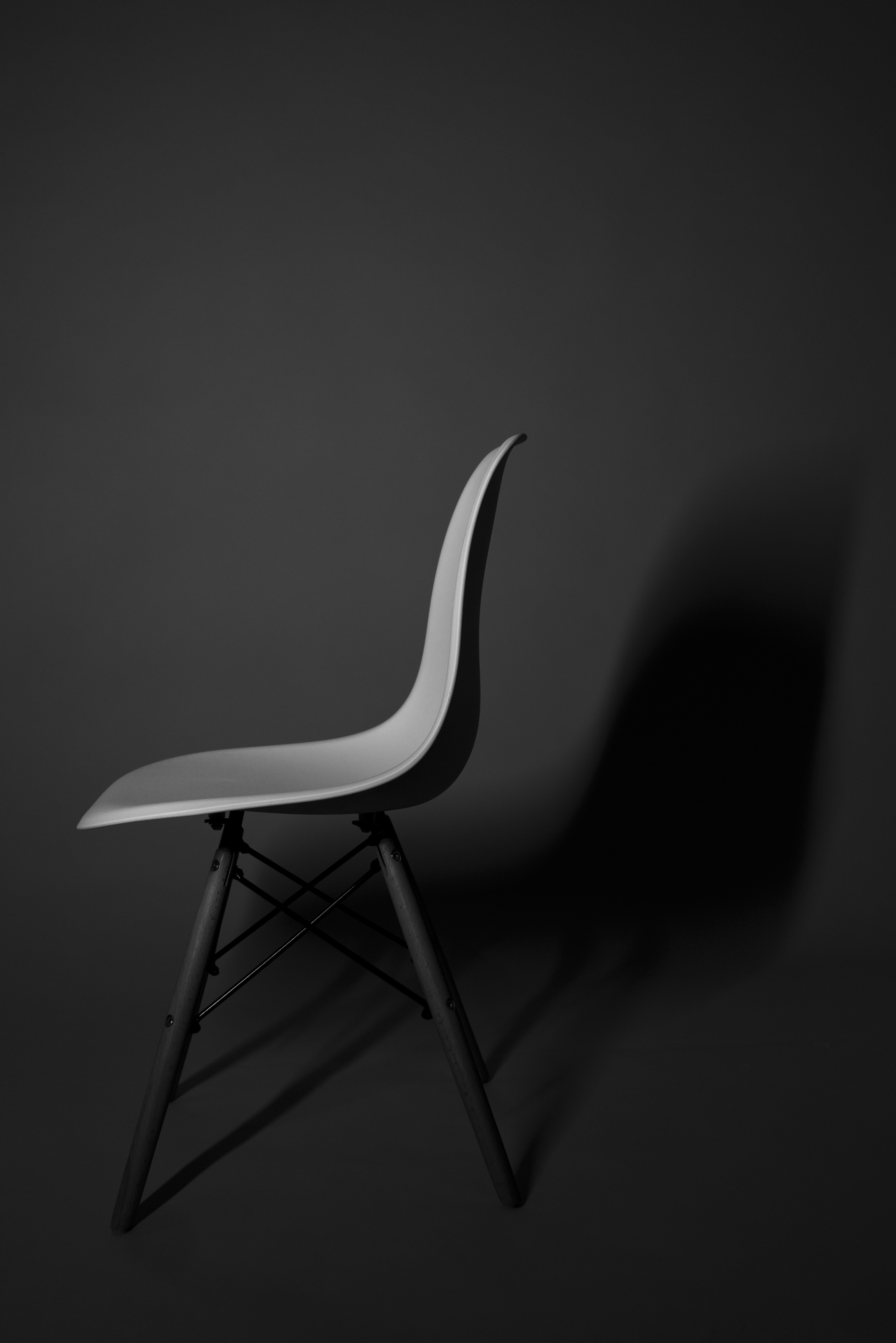 A sleek, modern chair casts a soft shadow against a dark backdrop, emphasizing its minimalist design and form.