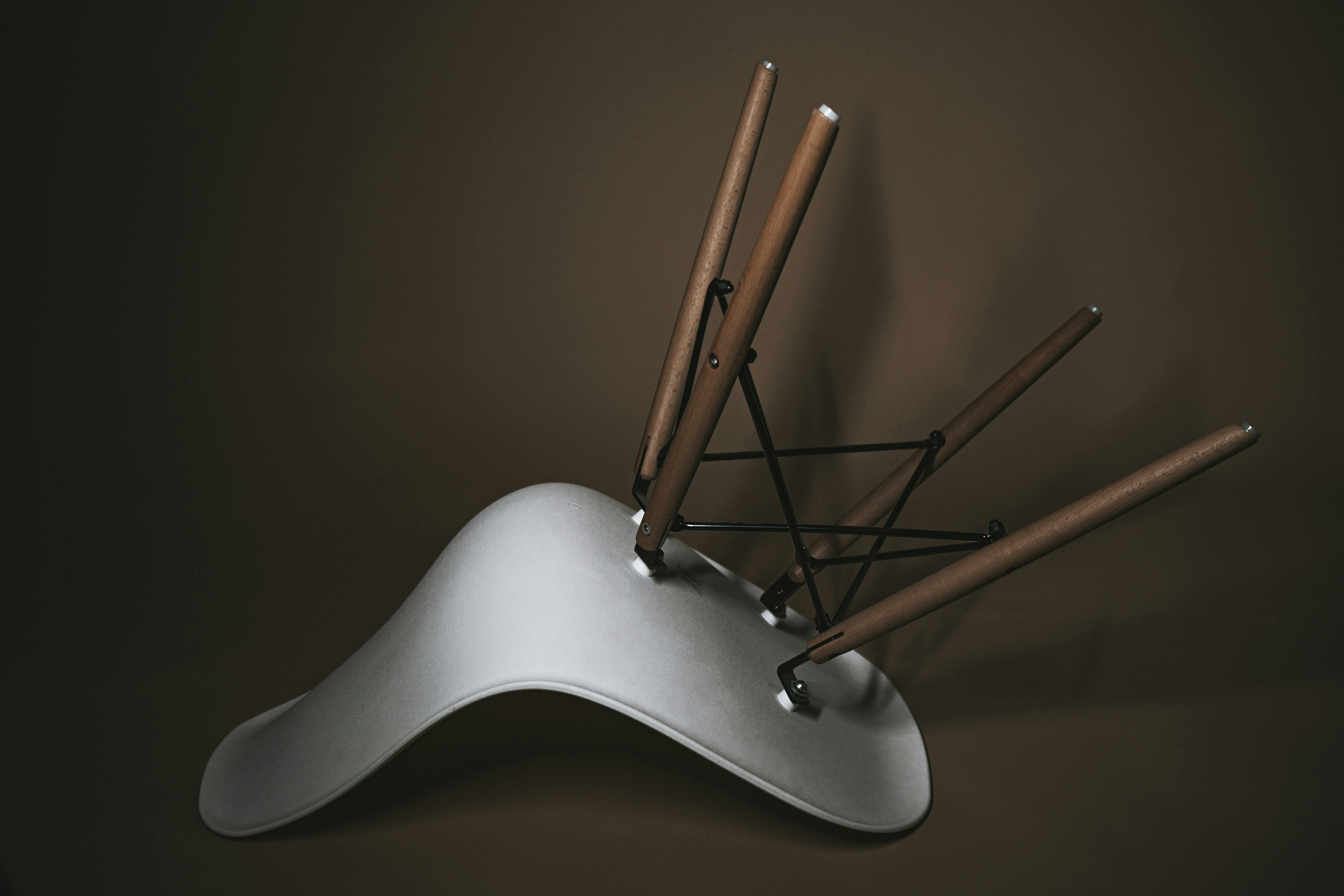 A modern chair flipped upside down, showcasing its sleek curves and wooden legs against a muted brown background.