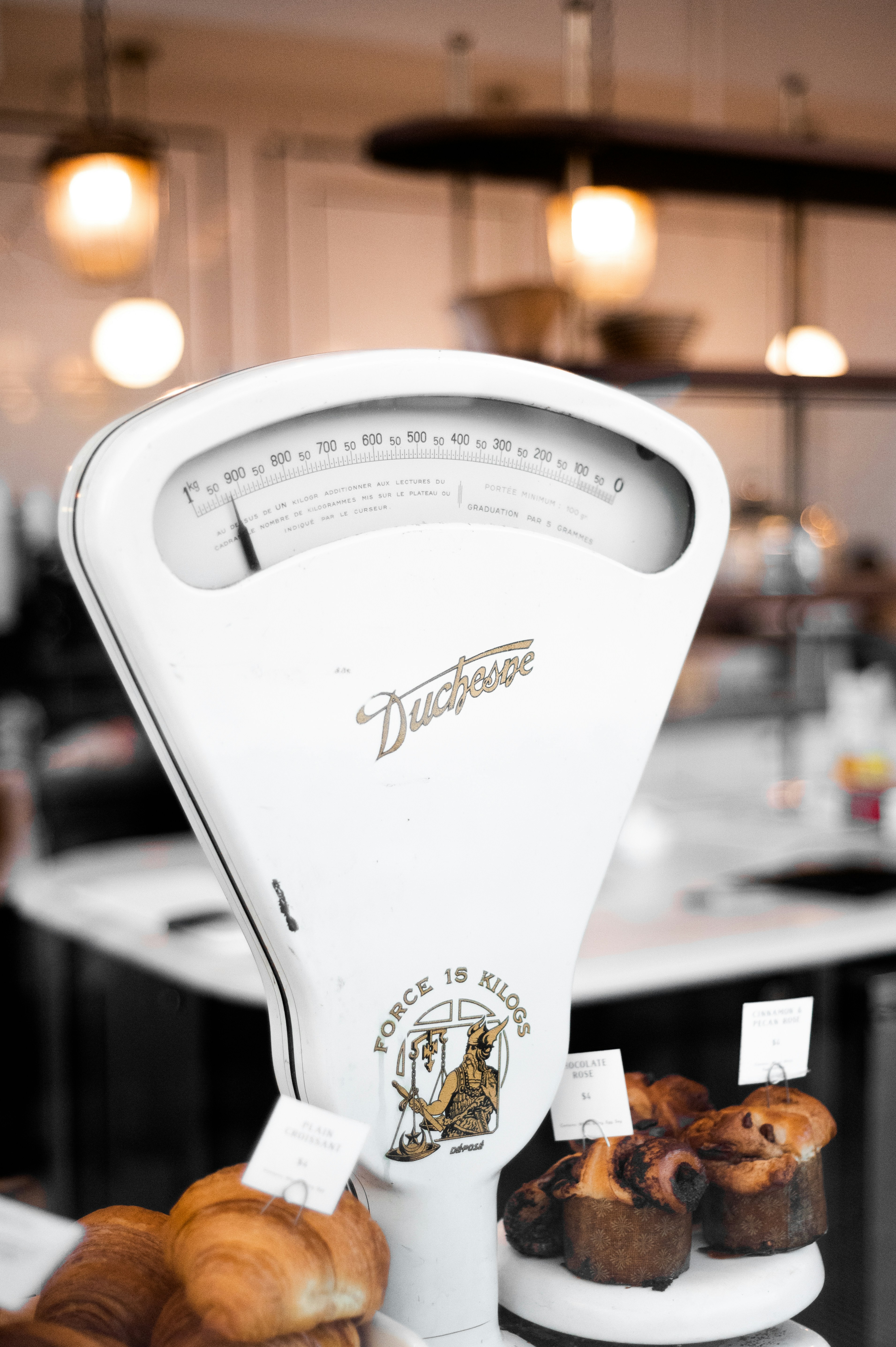 Vintage scale prominently displays baked goods in a cozy café setting. The scale's intricate design contrasts with the soft, blurred background.