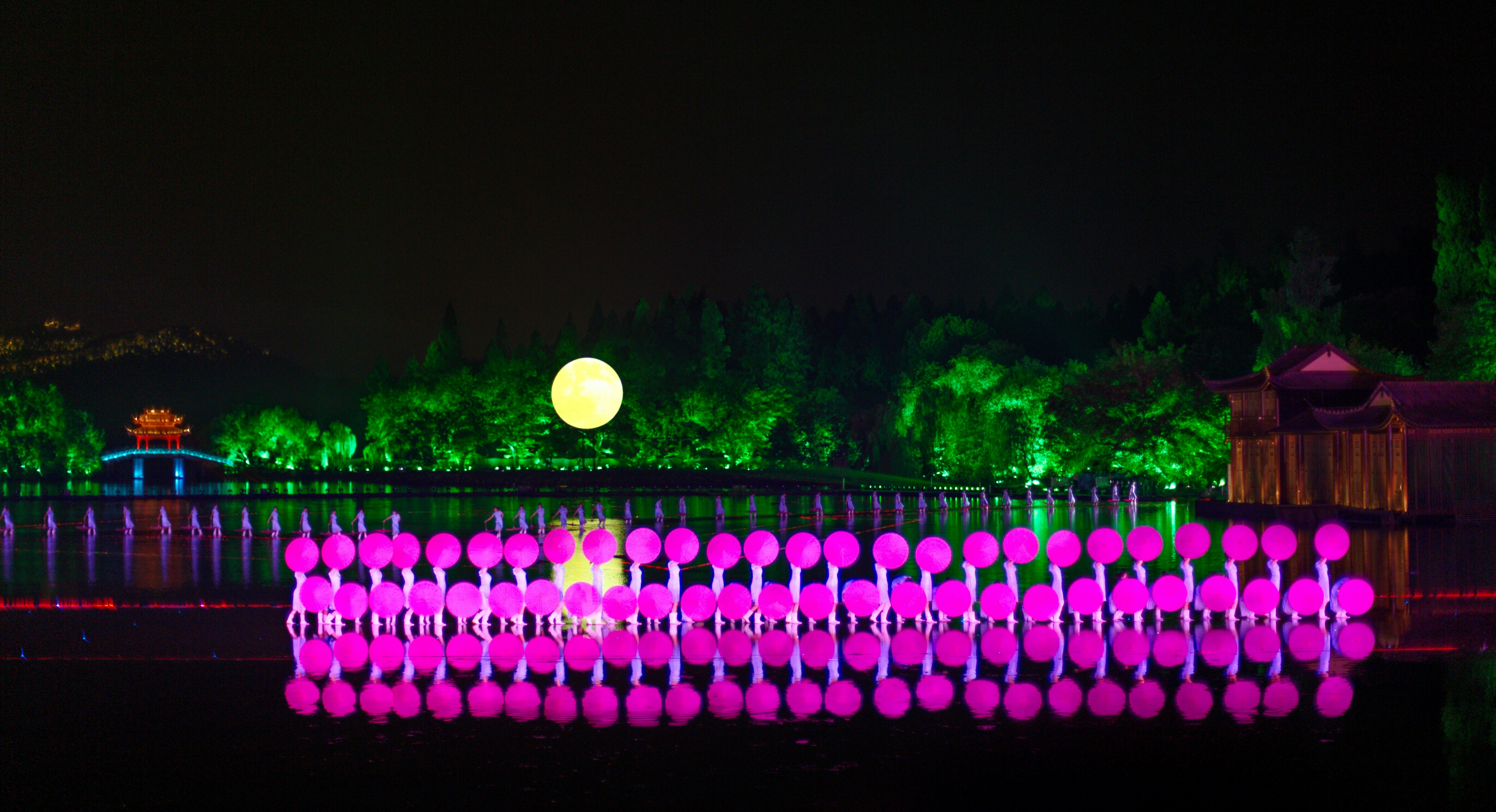 Illuminated lanterns cast vibrant reflections on the tranquil waters of West Lake under a dark night sky.