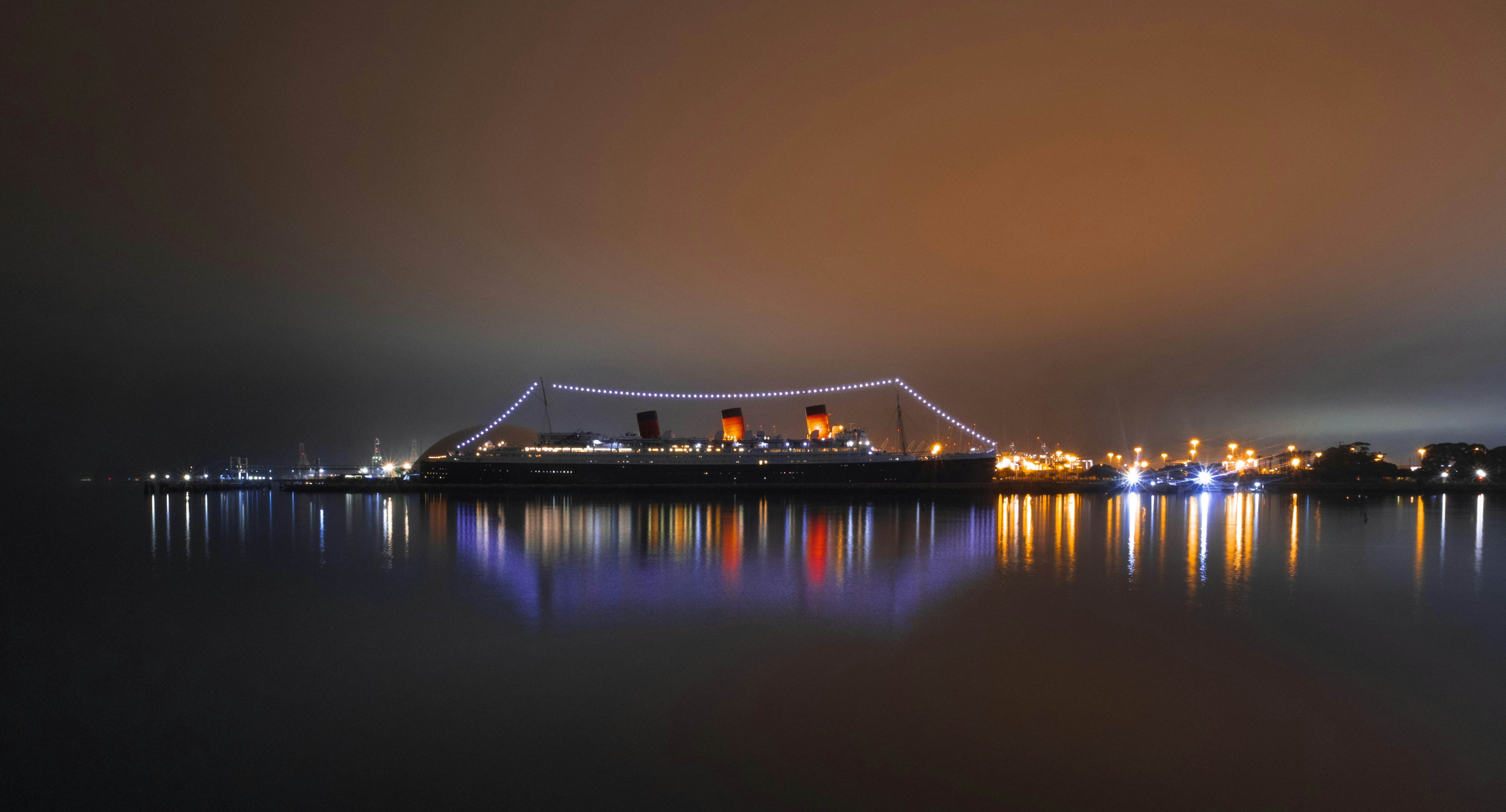 Illuminated cruise ship gliding through calm waters with a city bridge glowing in the background.
