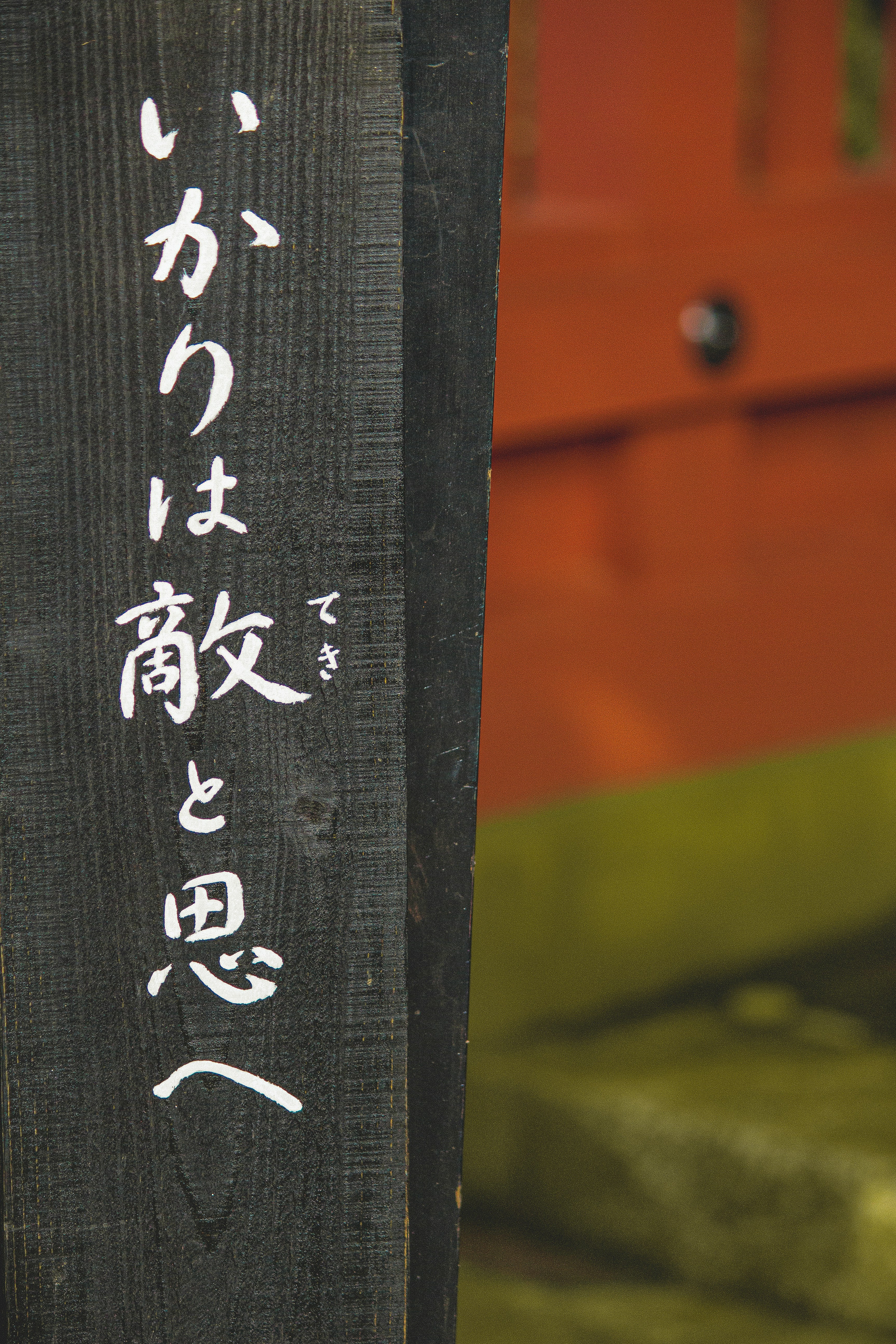 Japanese calligraphy on a wooden sign, set against a vibrant red backdrop, inviting contemplation. The text conveys a thoughtful message.