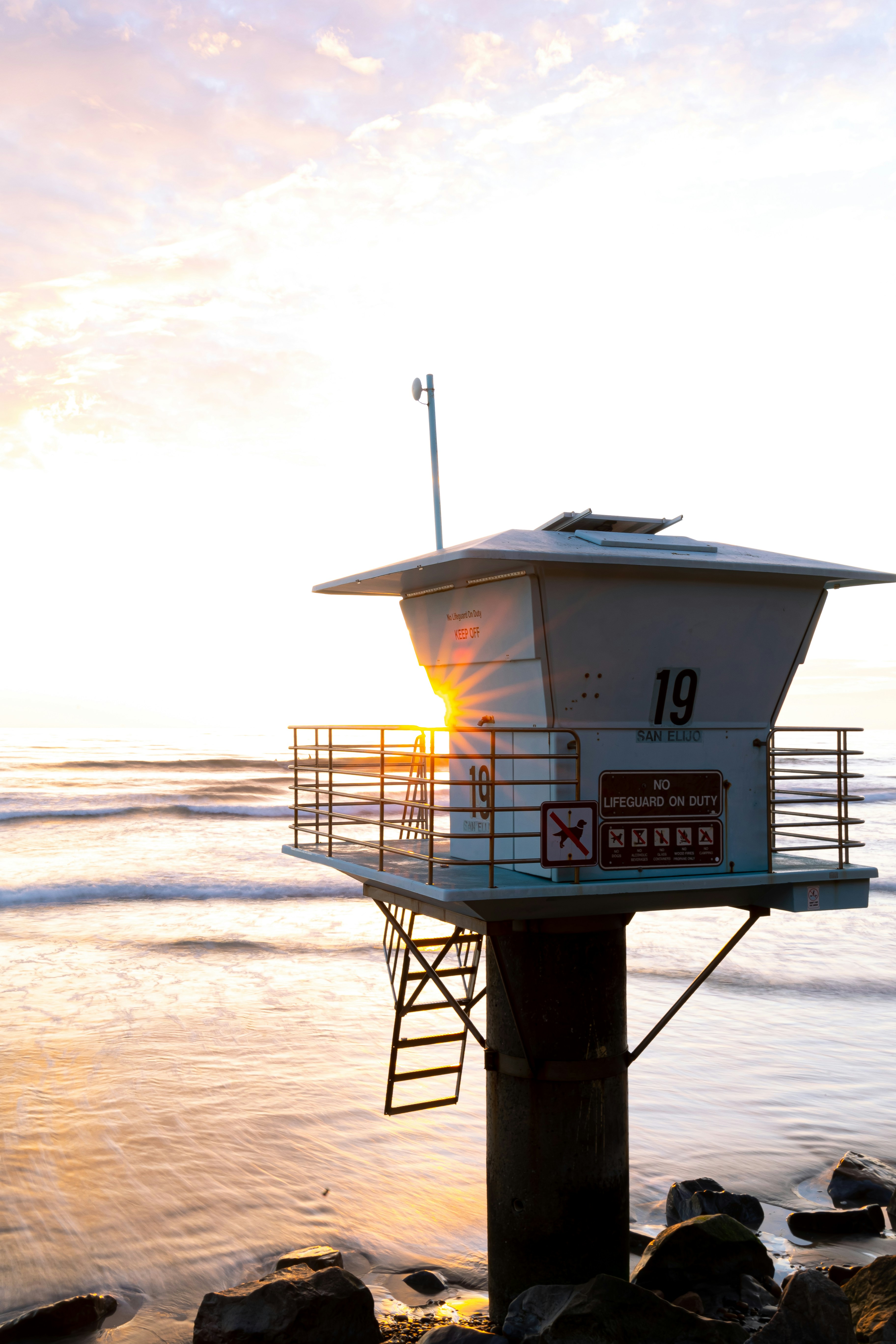 Lifeguard tower silhouetted against a vibrant sunset, casting a warm glow as waves gently lap at the shore.