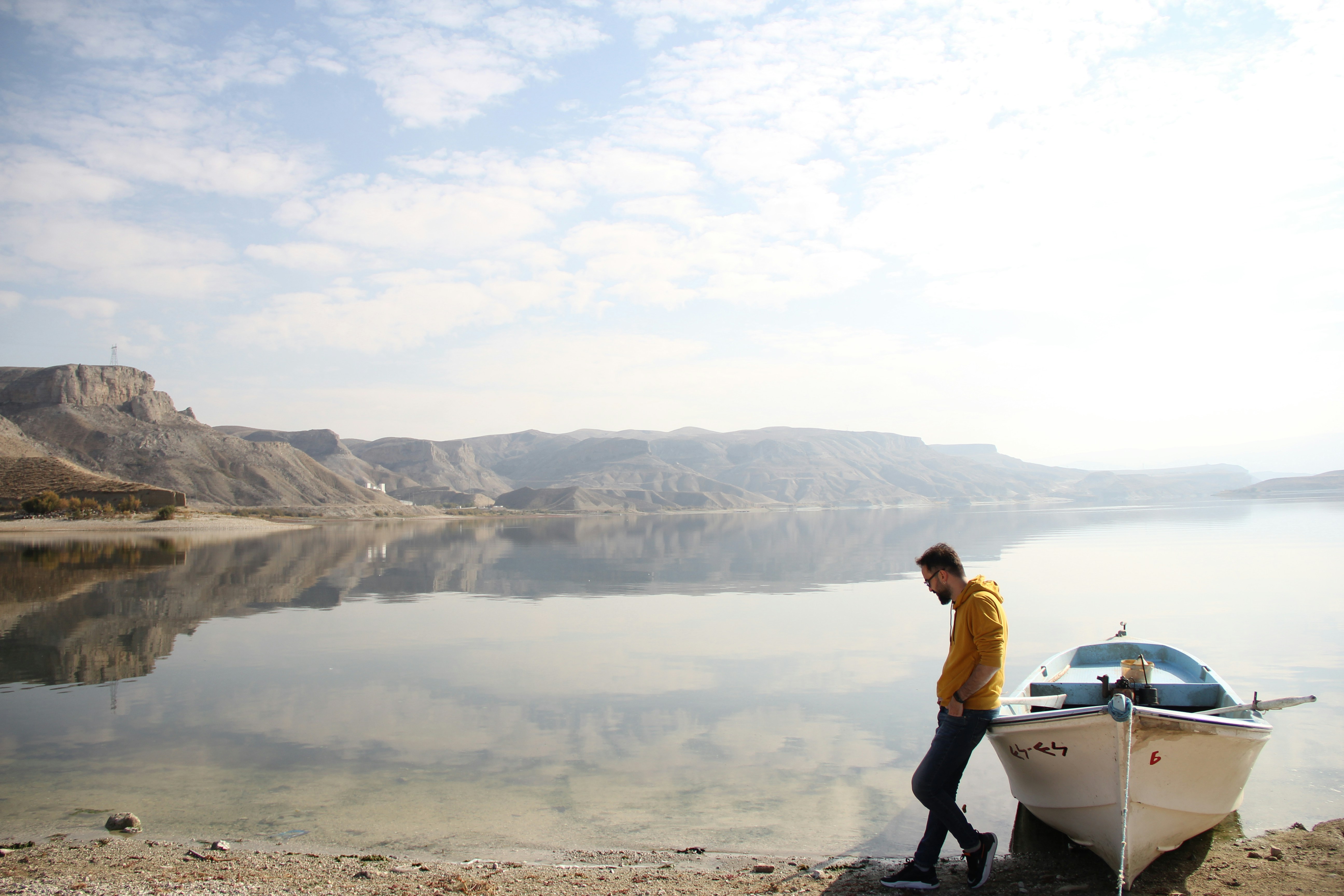 Guy standing on a boat with mountain reflections on lake.