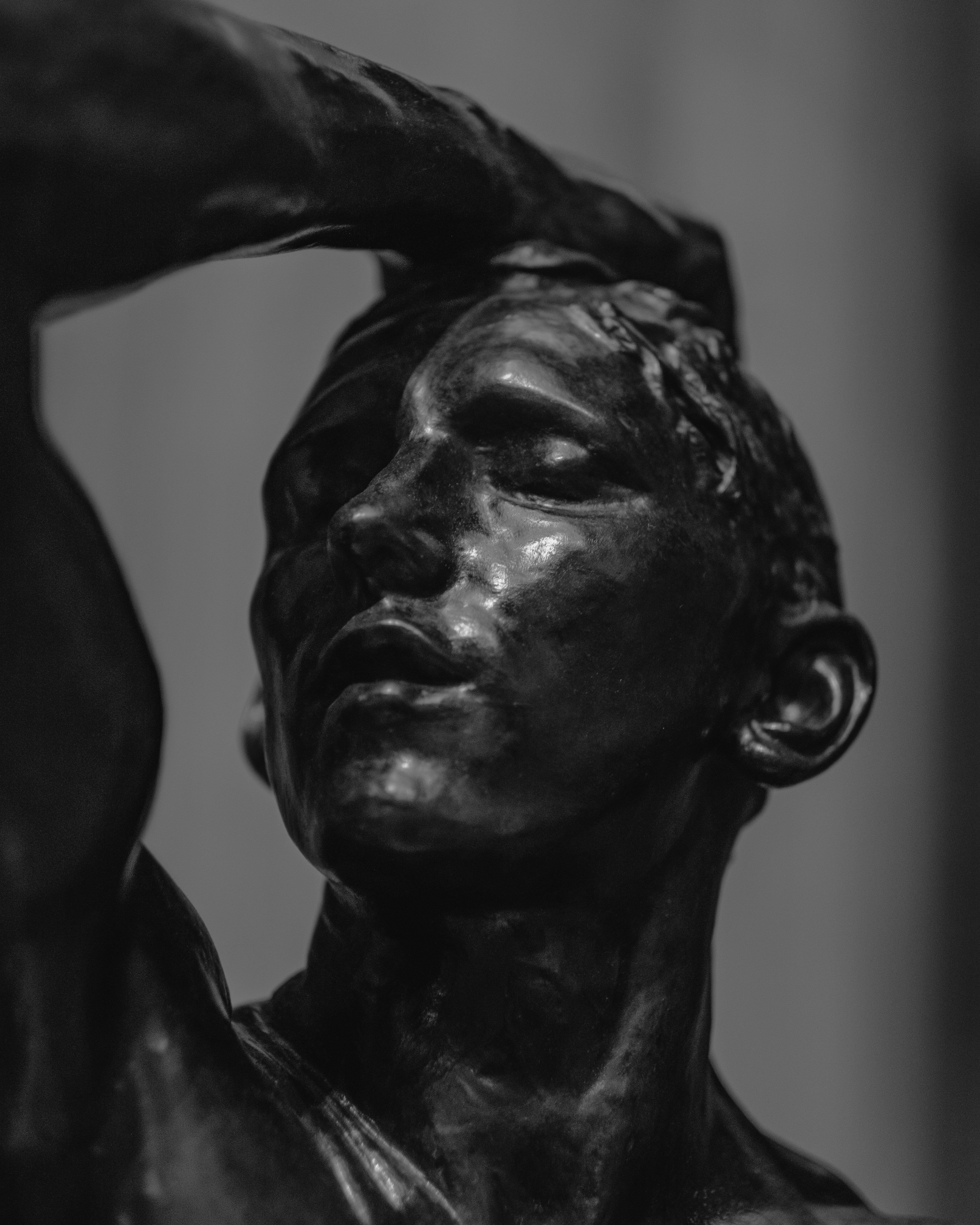 Close-up of a bronze sculpture depicting a figure in a moment of introspection, showcasing intricate details and textures. The artwork captures the essence of human emotion.