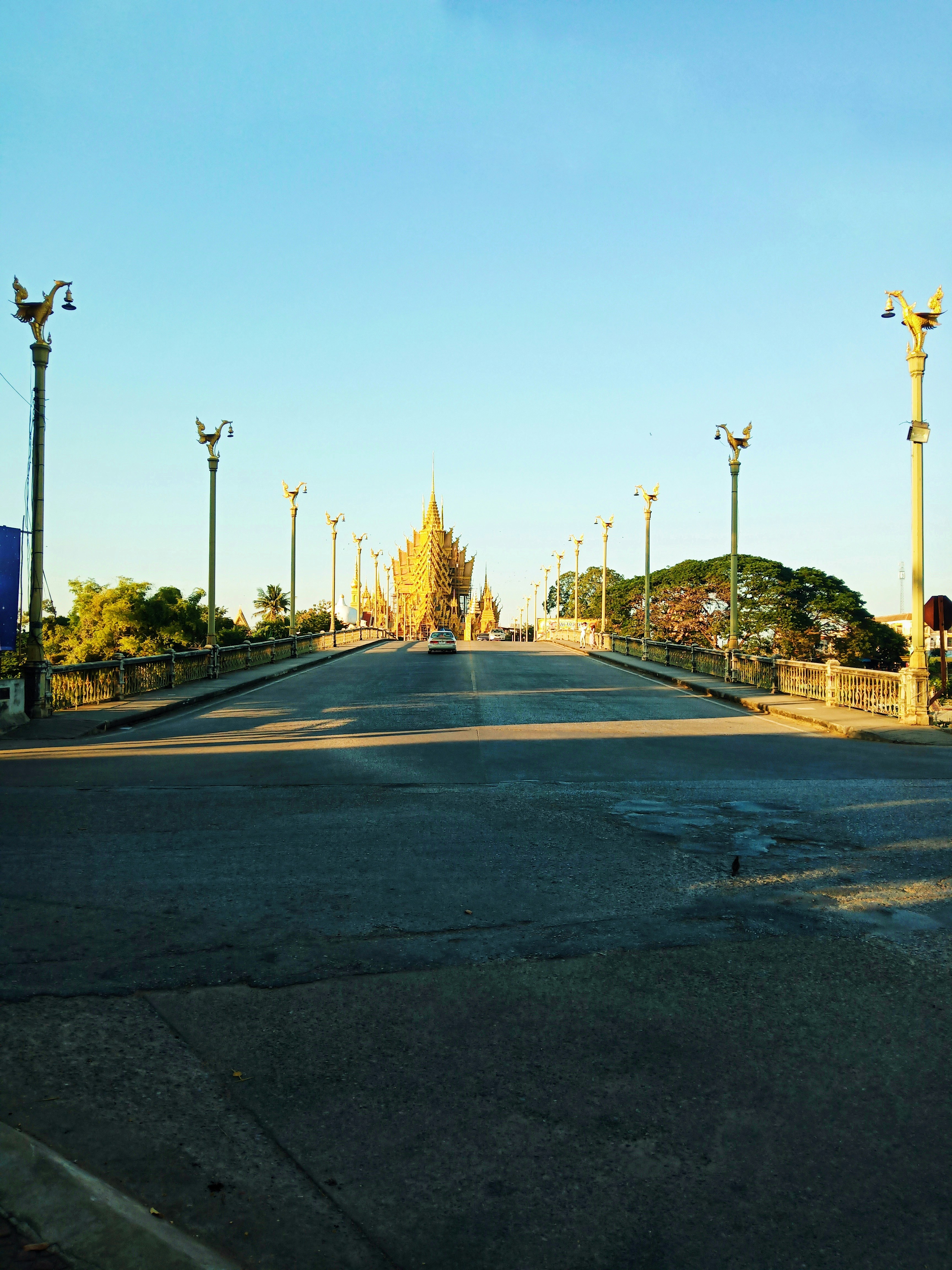 Golden temple viewed across a bridge lined with ornate lamp posts under a clear blue sky.