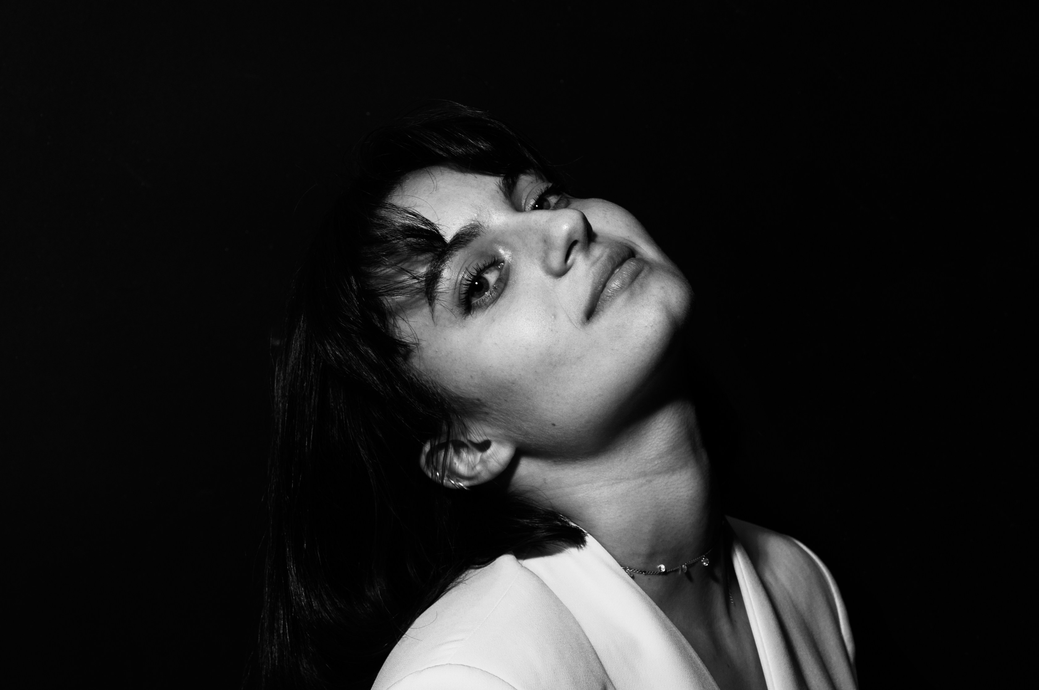 Black and white portrait of a woman with her eyes gently closed against a dark background.
