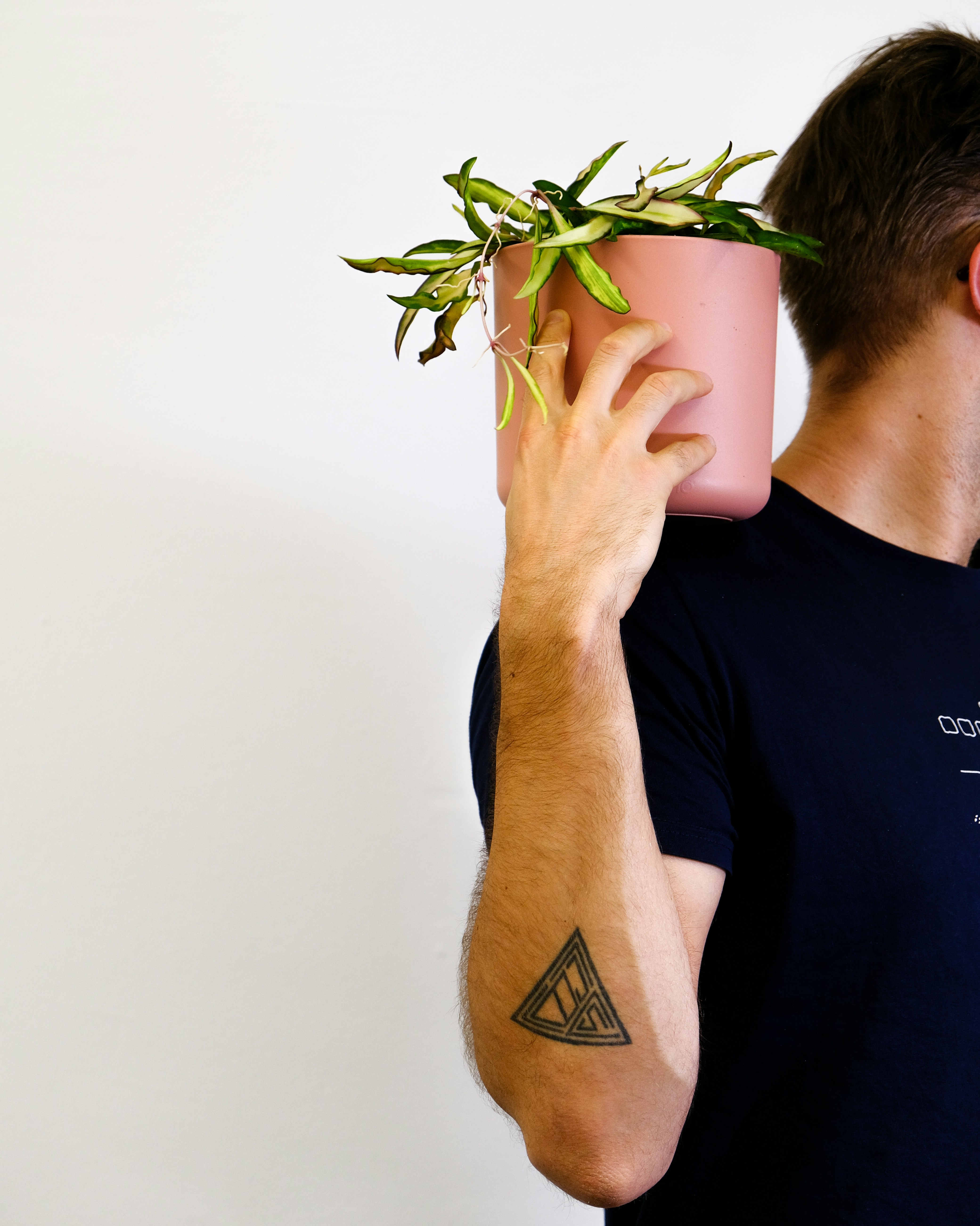 Person holding a potted plant close to their shoulder against a minimalistic backdrop. The focus is on the harmonious blend of human and nature.