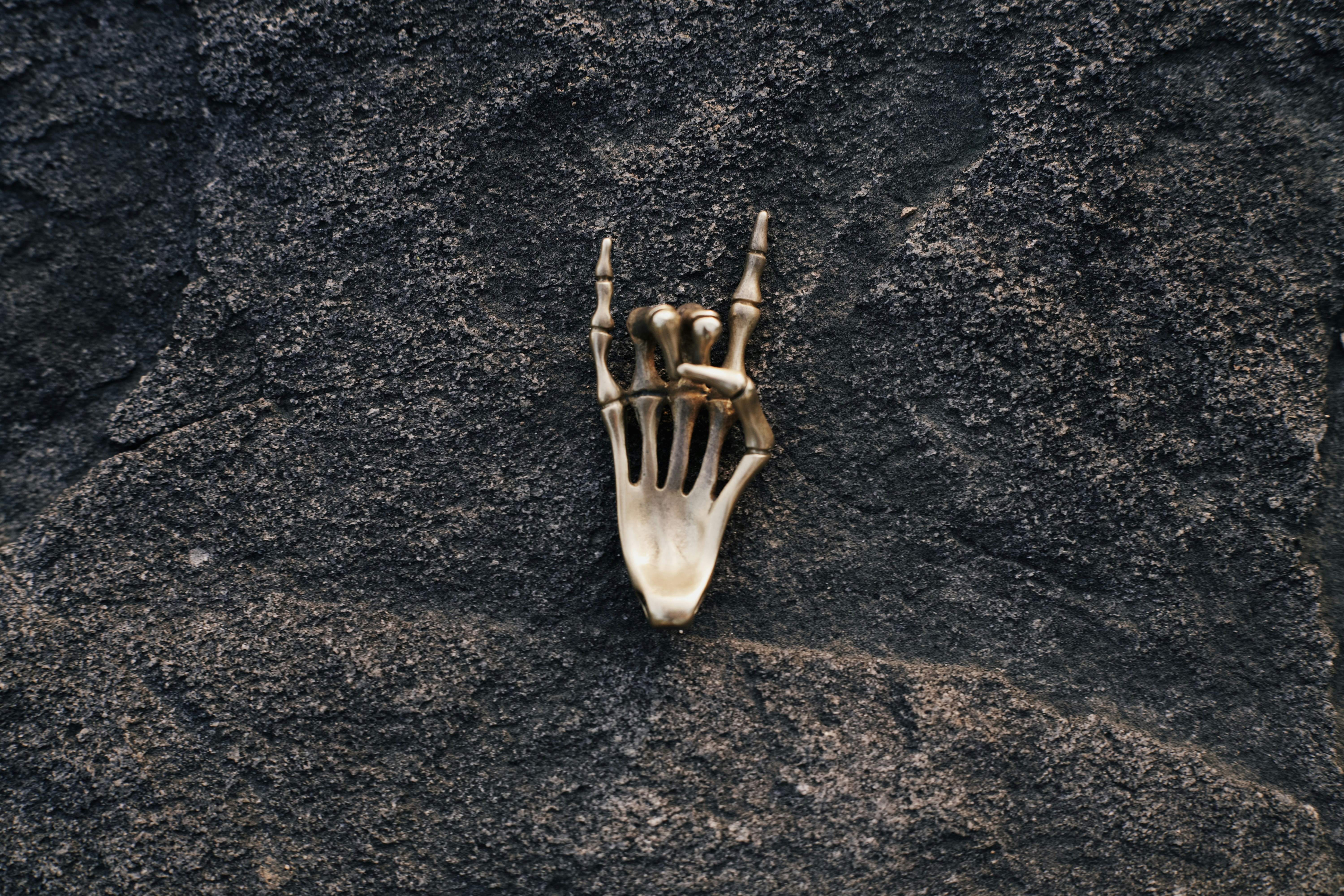 A metallic hand sculpture making a rock-and-roll gesture against a textured stone background.