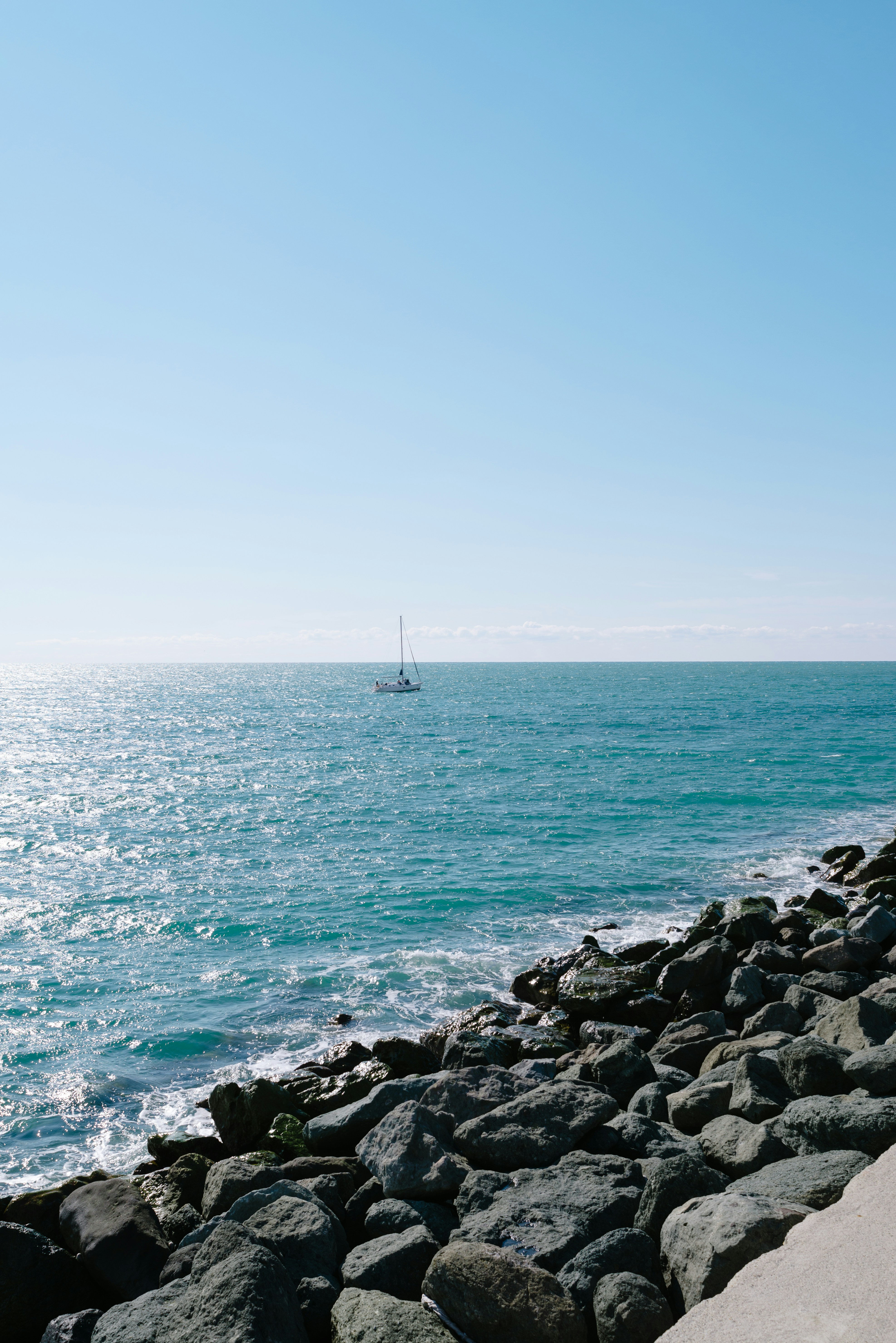 A sailboat glides across the turquoise waters, framed by a rocky shoreline under a clear blue sky.