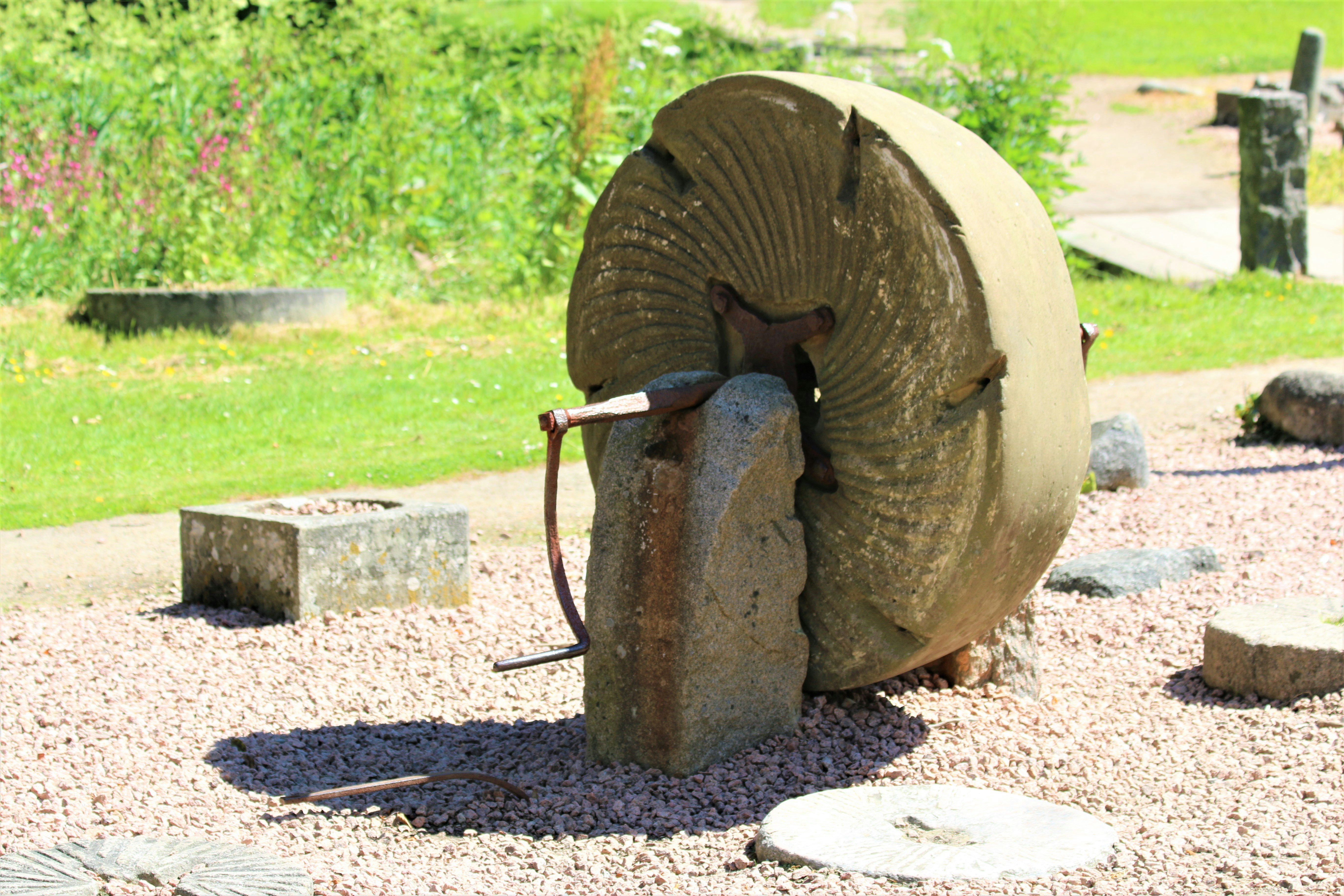 Ancient grinding mill in sunlit park setting with rusted iron bar