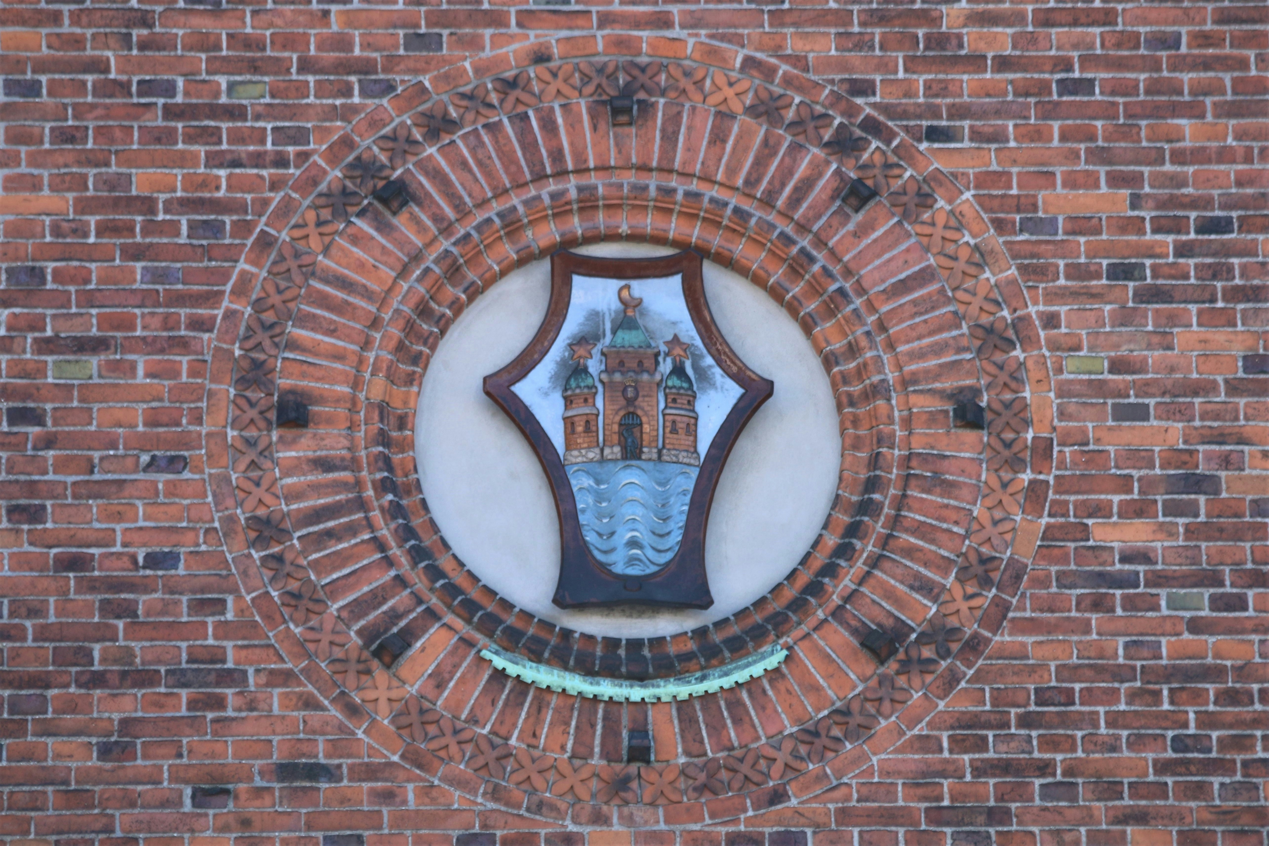 Intricate coat of arms set against a textured brick backdrop, showcasing architectural artistry and historical significance.