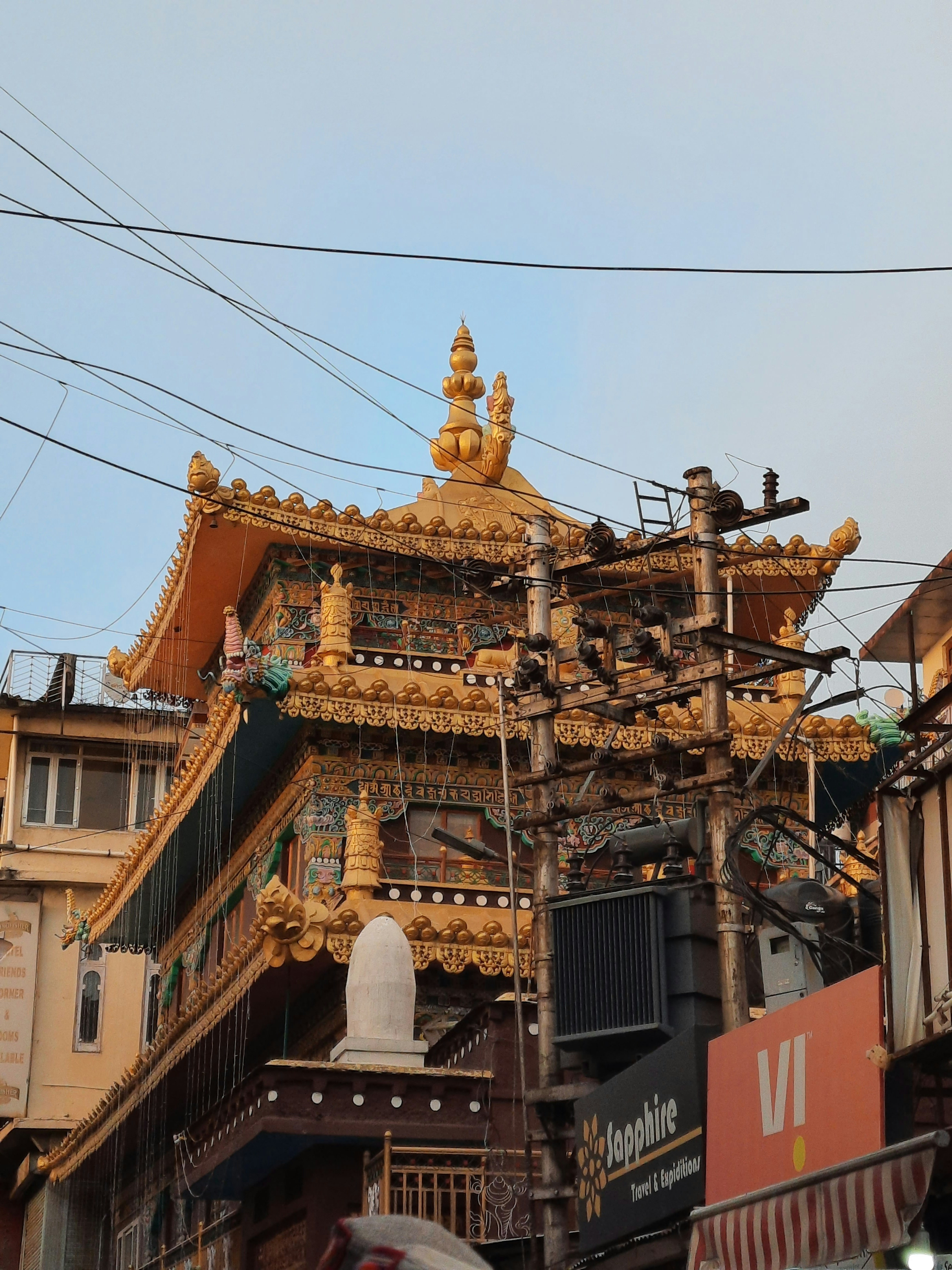 Ornate golden temple rooftop rises above tangled power lines on a busy street.