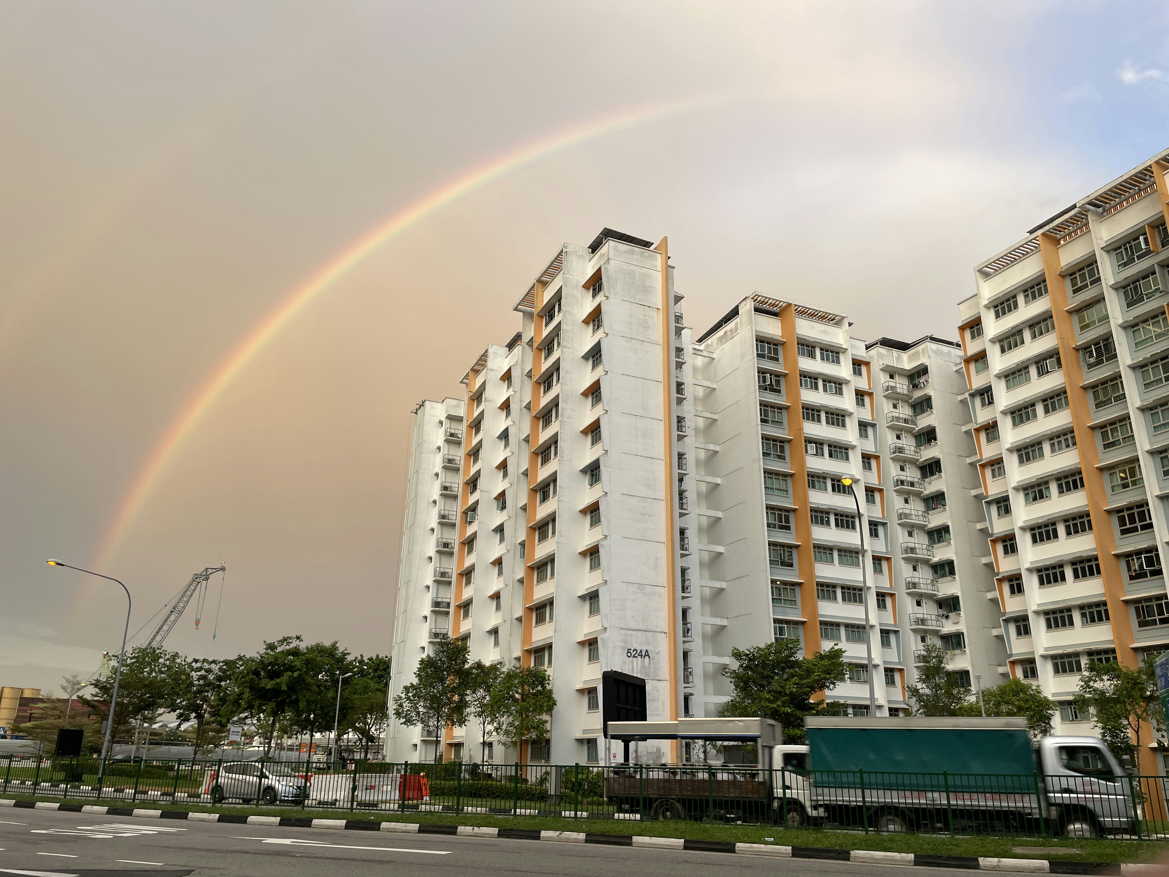 Rainbow arches over high-rise buildings with a crane and trees in the foreground.