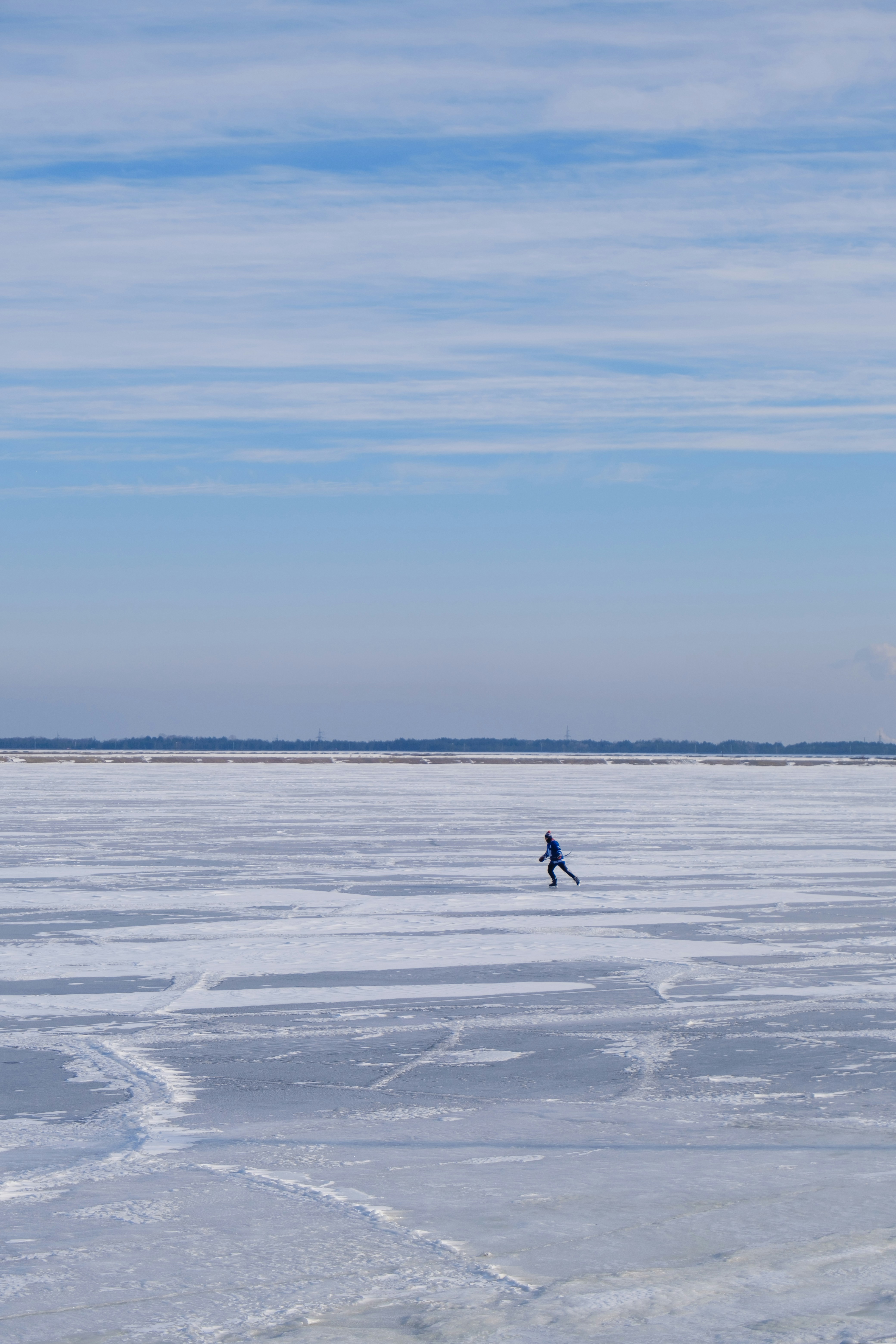 A solitary figure ice skating on a vast frozen lake under a clear blue sky.