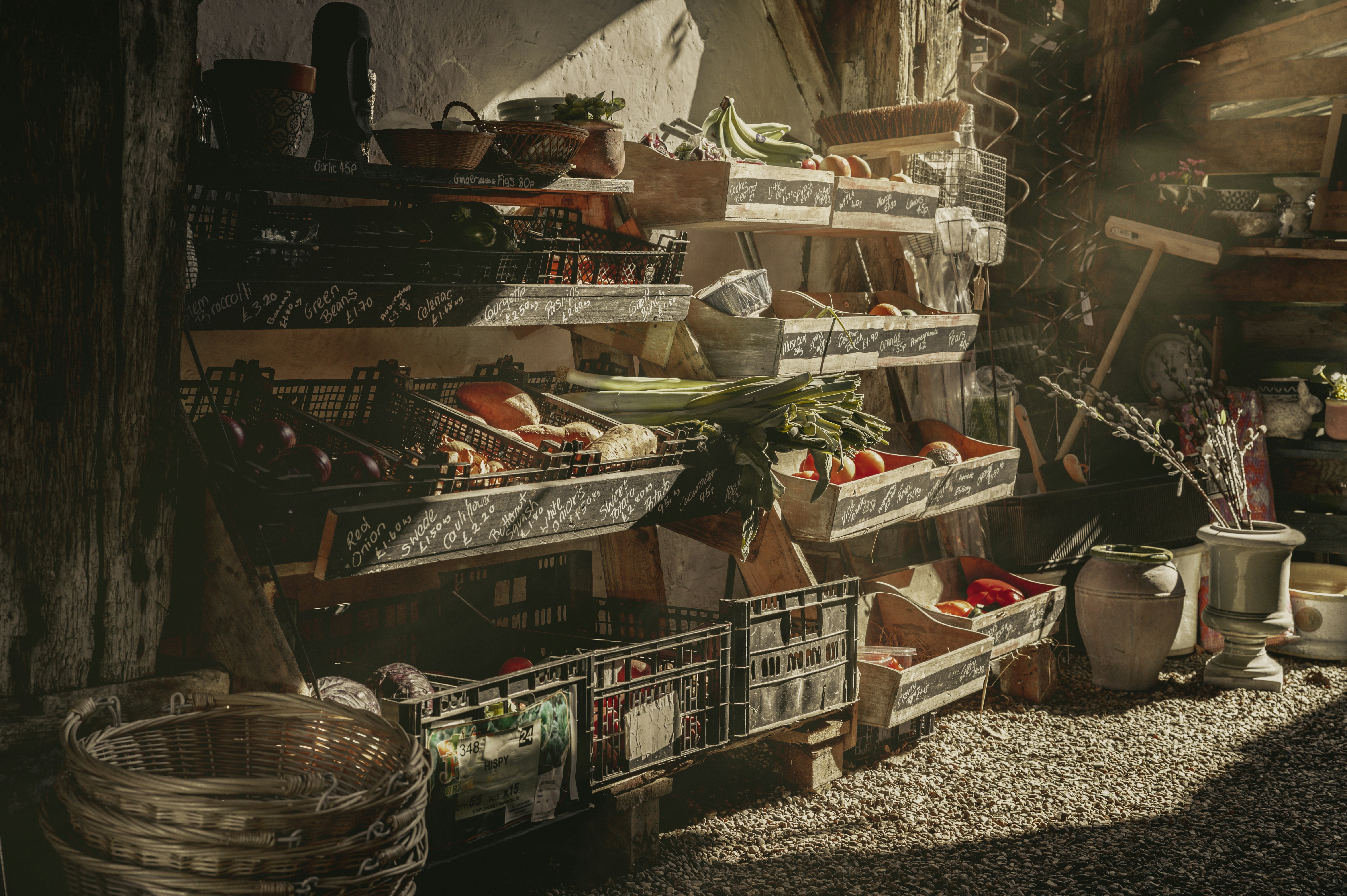 Vibrant assortment of fresh vegetables and herbs arranged on wooden shelves in a rustic market setting. Sunlight filters through, enhancing the warm tones.