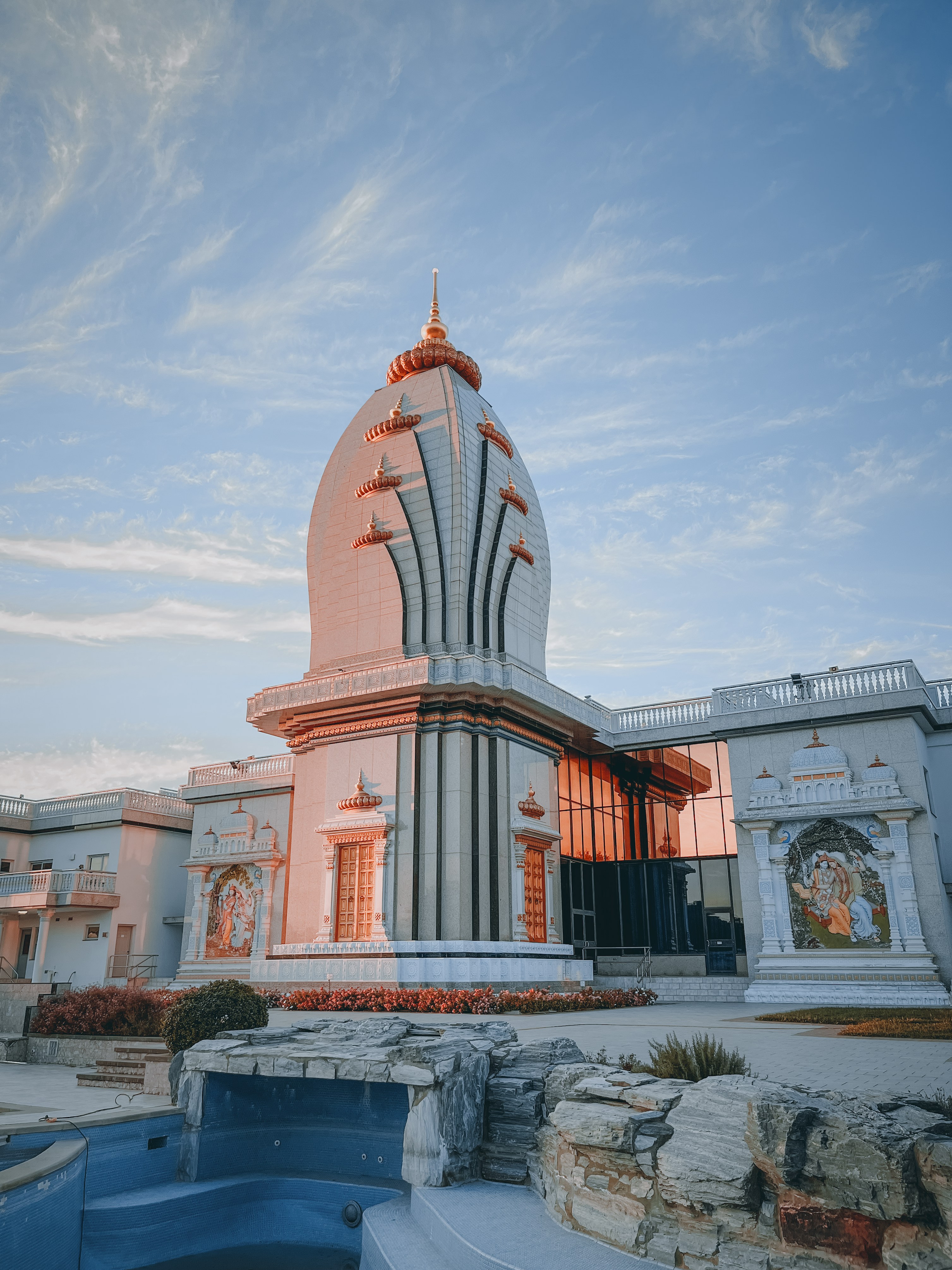 A beautifully crafted temple structure with intricate designs and modern glass elements, set against a serene sky. The juxtaposition of traditional and contemporary architecture is striking.