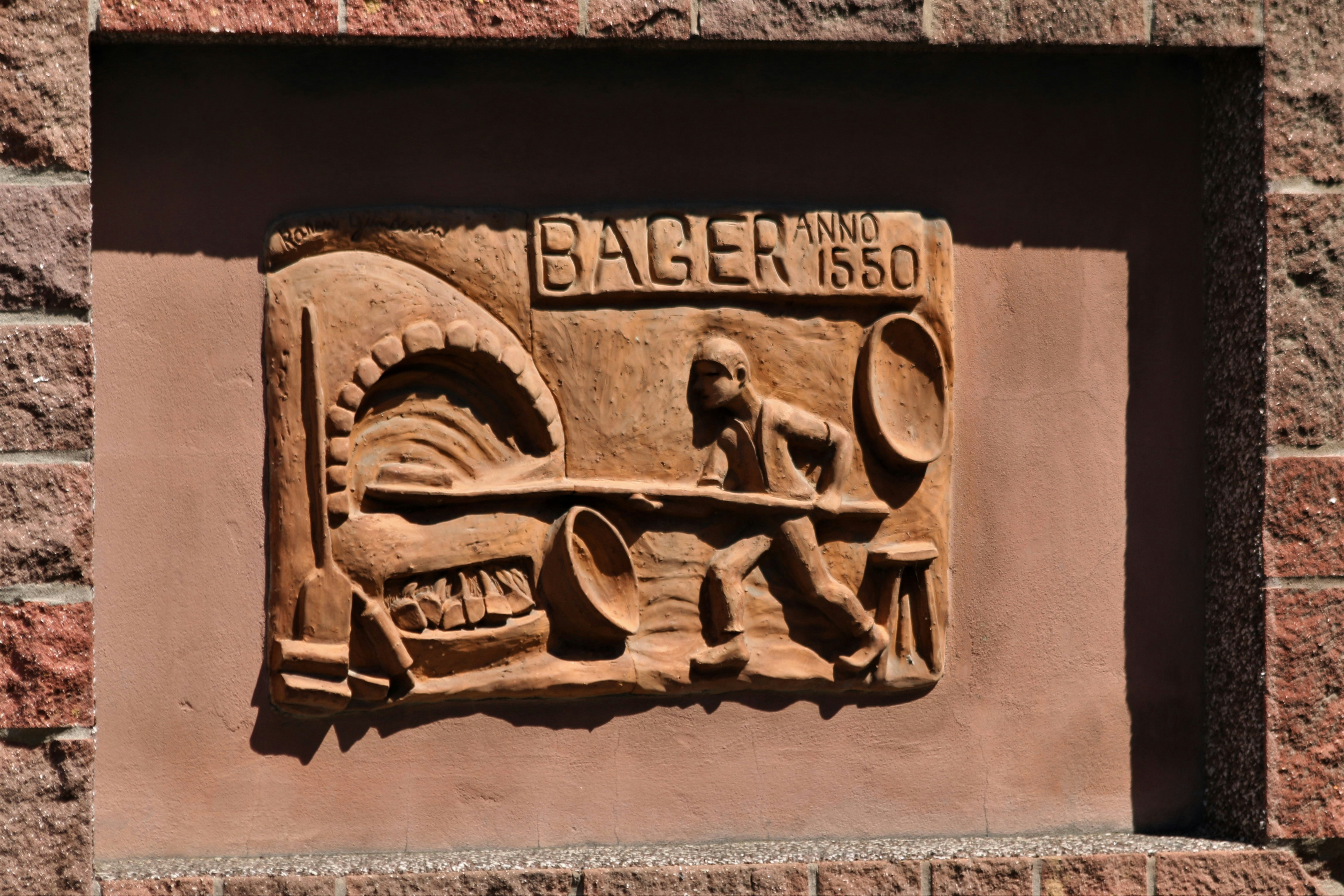 Relief sculpture depicting a baker at work, showcasing traditional baking tools and an oven, inscribed with 'BAGER ANNO 1550.'