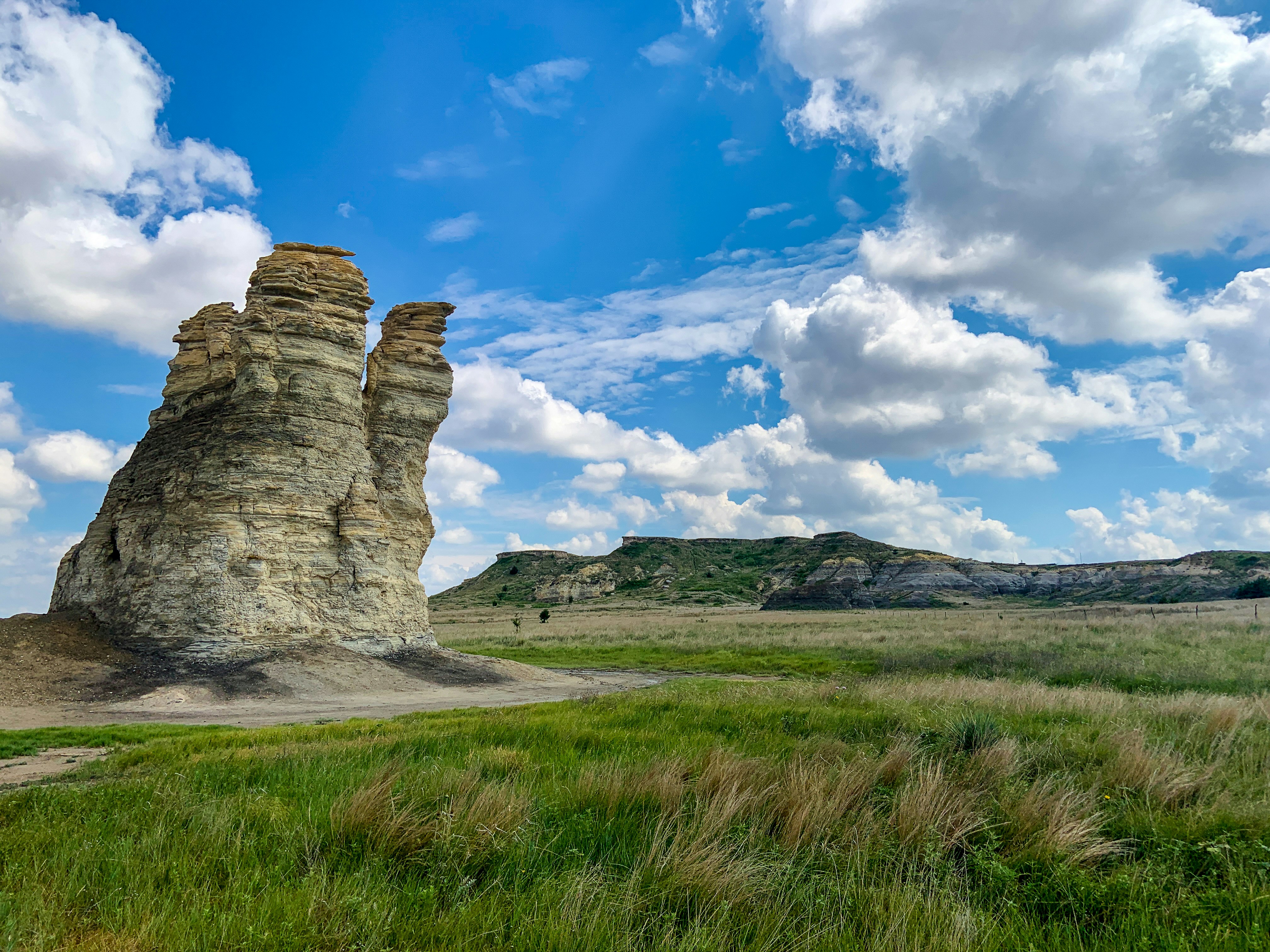 Towering rock formations rise from a grassy field under a vibrant blue sky with scattered clouds.