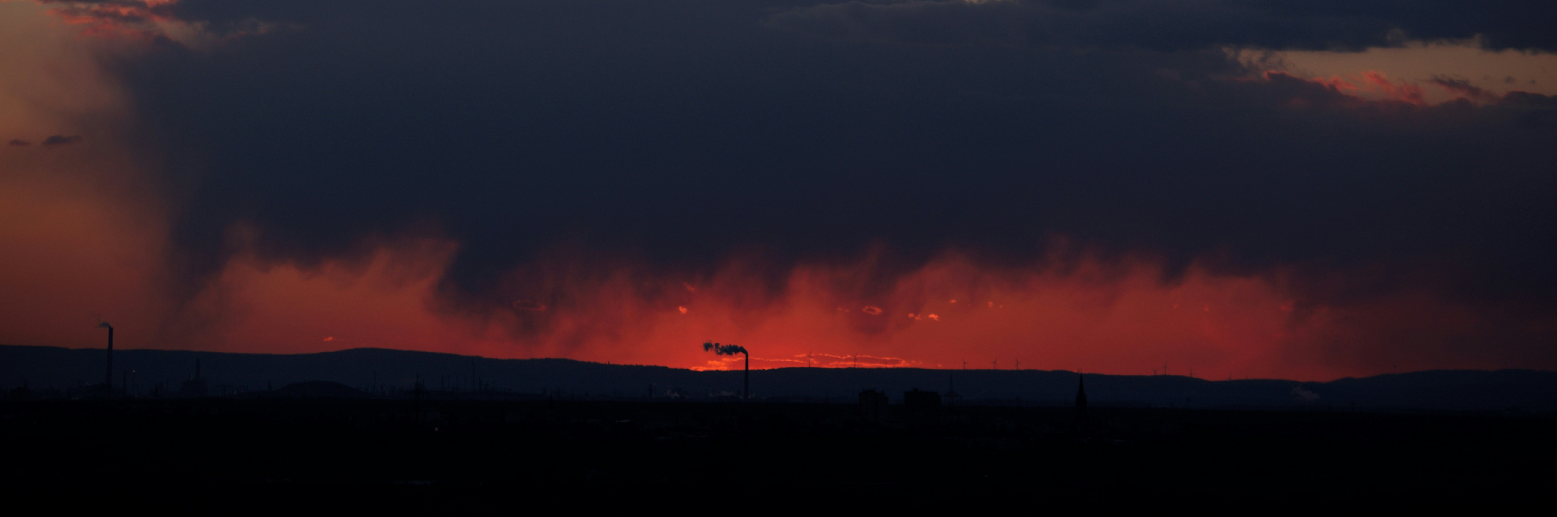 Dark clouds loom over a horizon ablaze with fiery hues as twilight descends, creating a dramatic contrast in the sky.