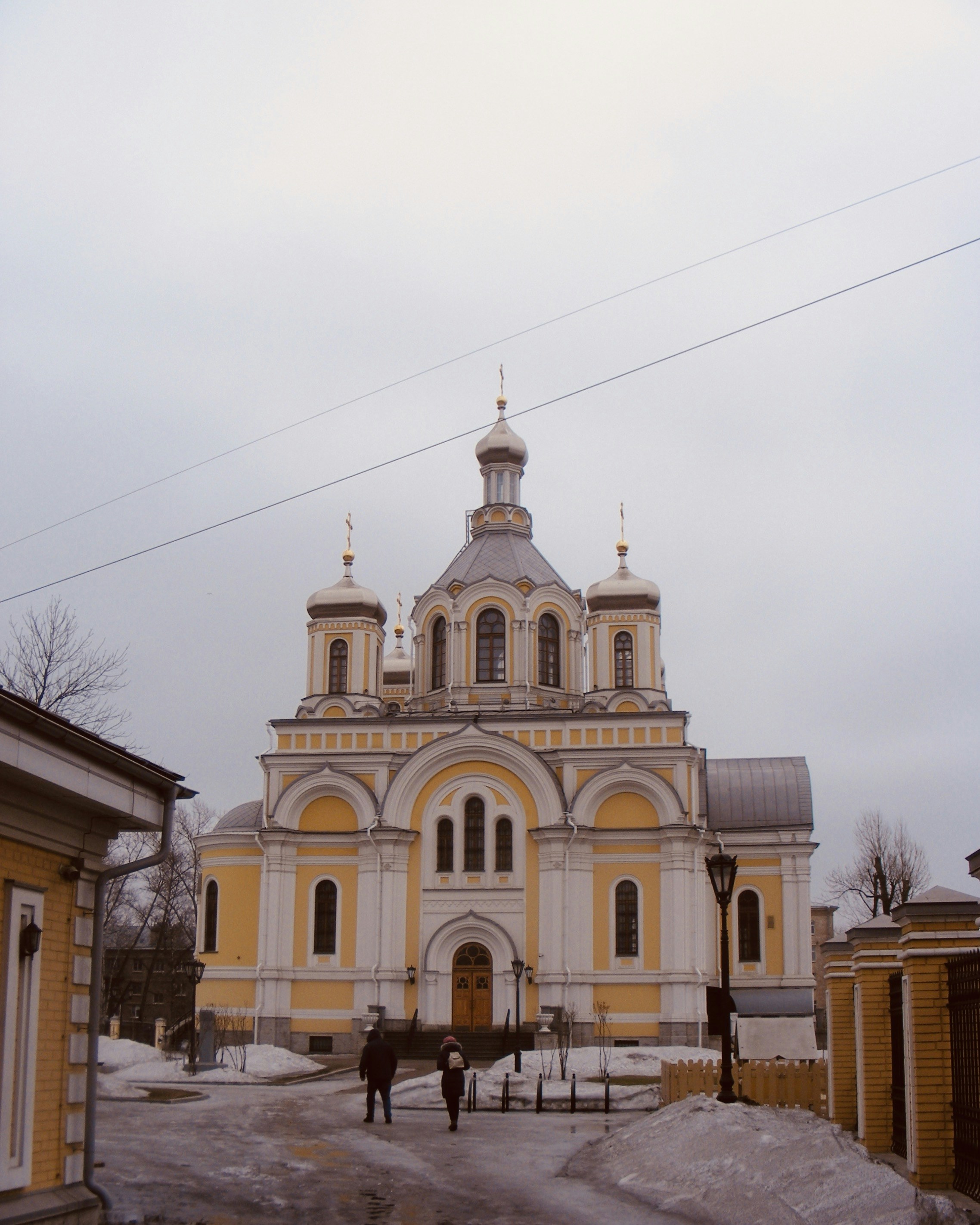 Elegant church with yellow and white façade, framed by a winter landscape and cloudy sky.