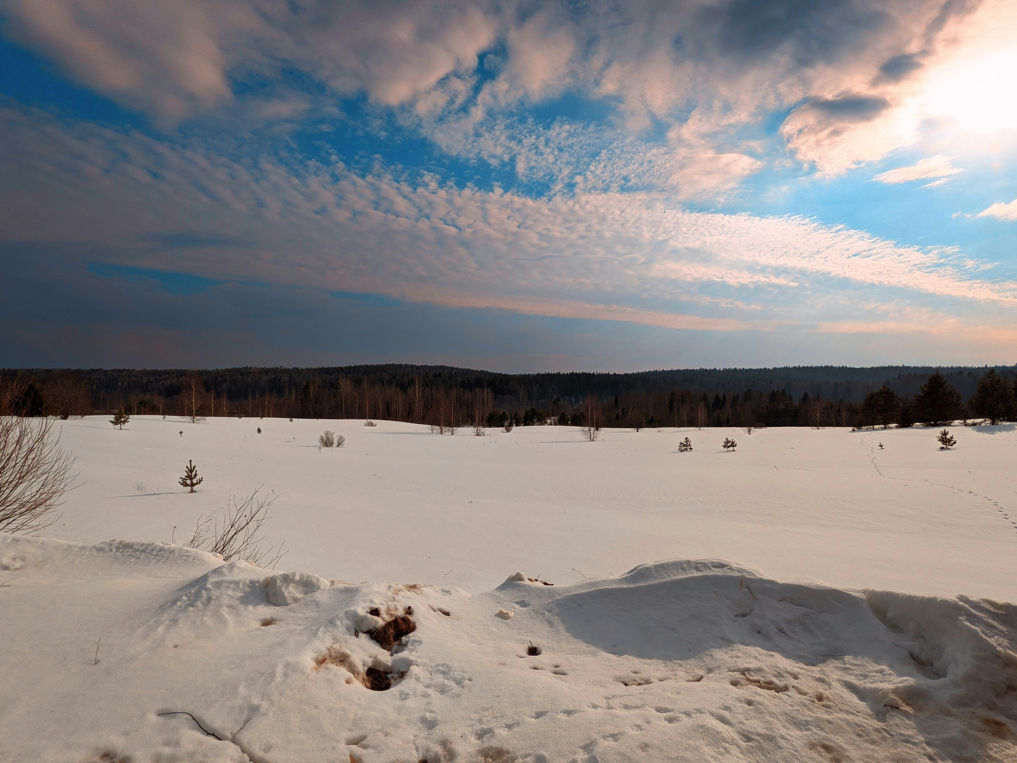 Expansive snow-covered field beneath a dramatic sky with streaked clouds and hints of sunlight.