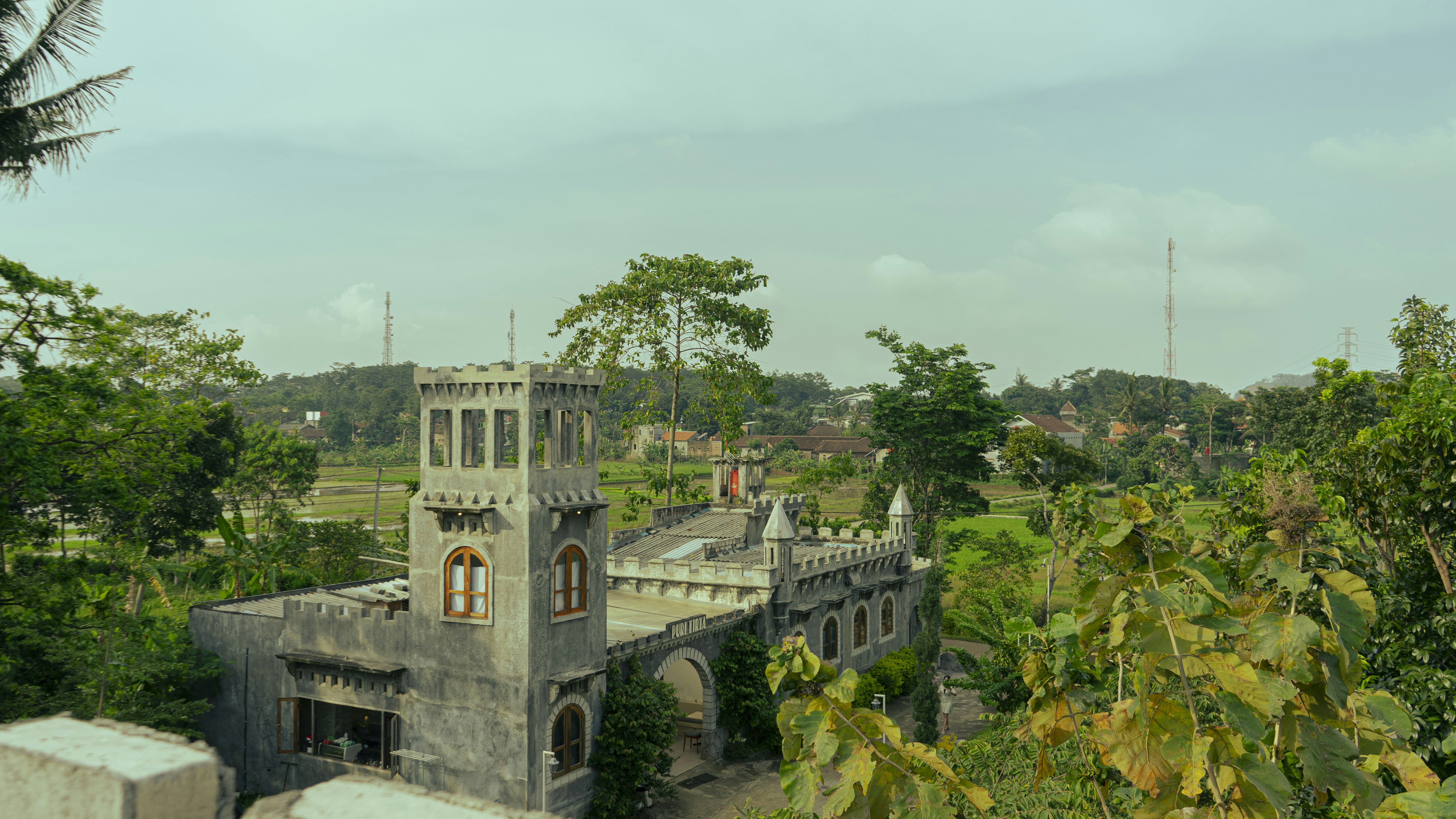 An old building with a central tower surrounded by lush green trees.