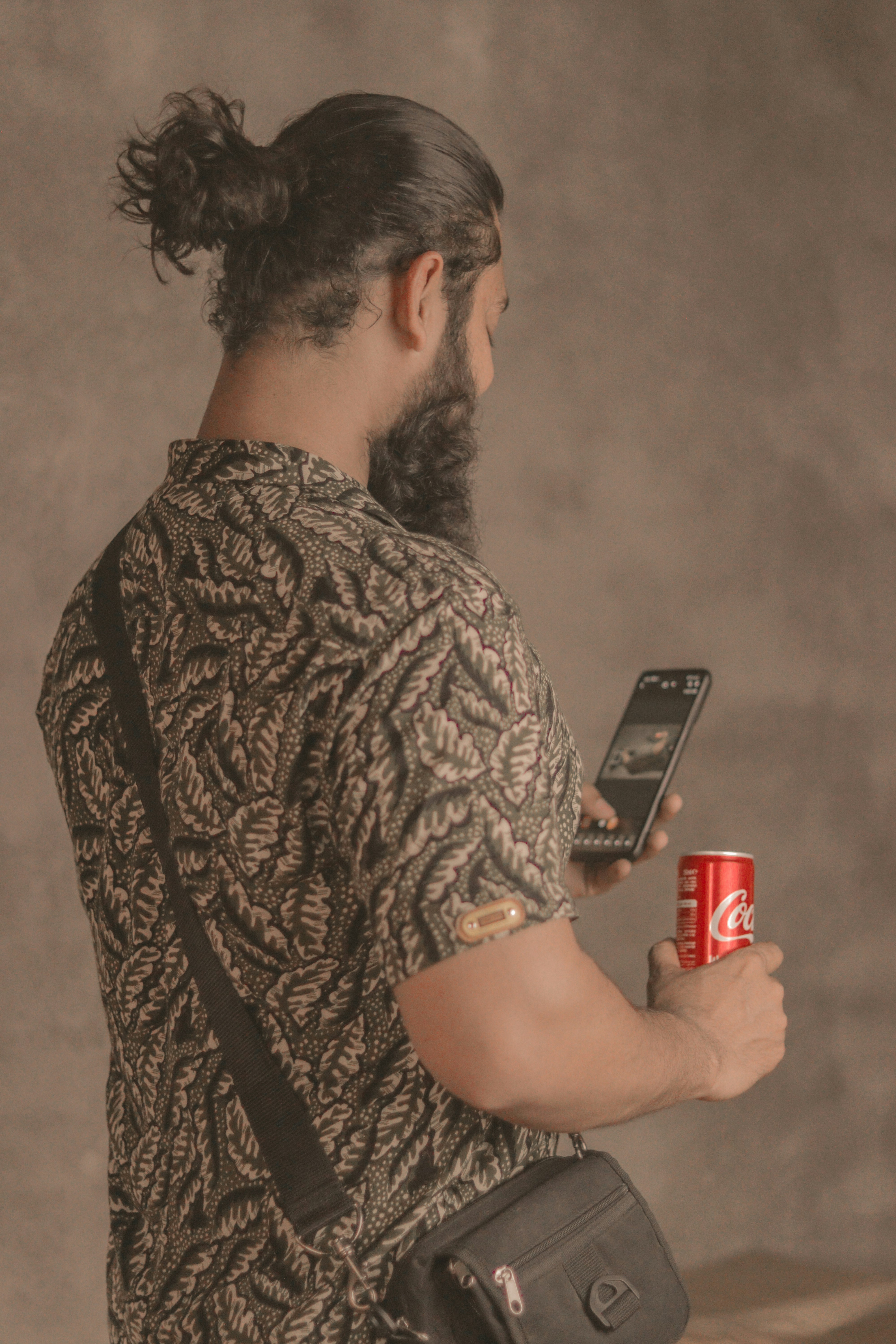 Fern-patterned Confidant: a back-turned portrait of a bearded man with phone and cola