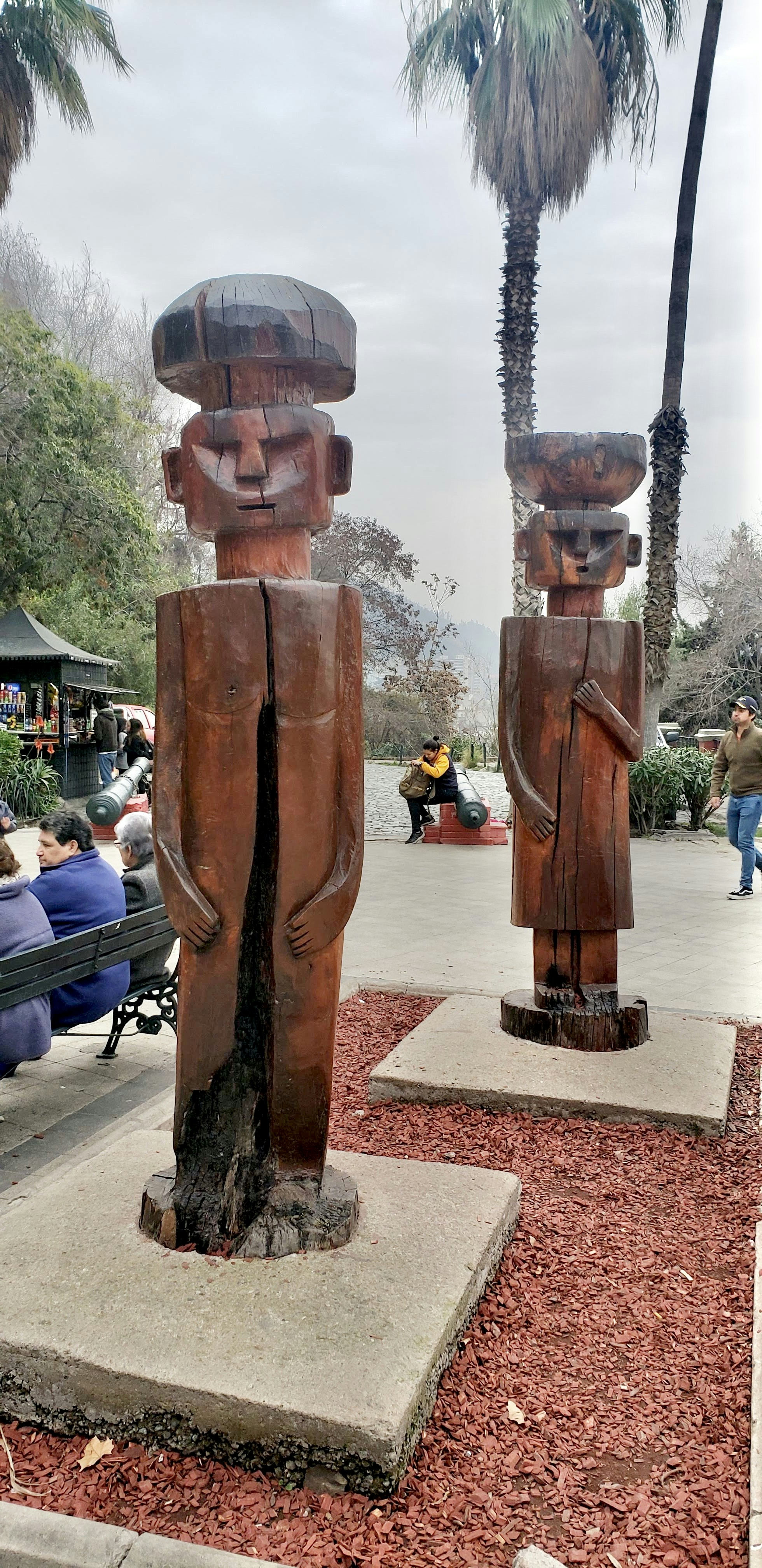 Carved Wooden Figures in a Park: Standing Sentinels by the Palm