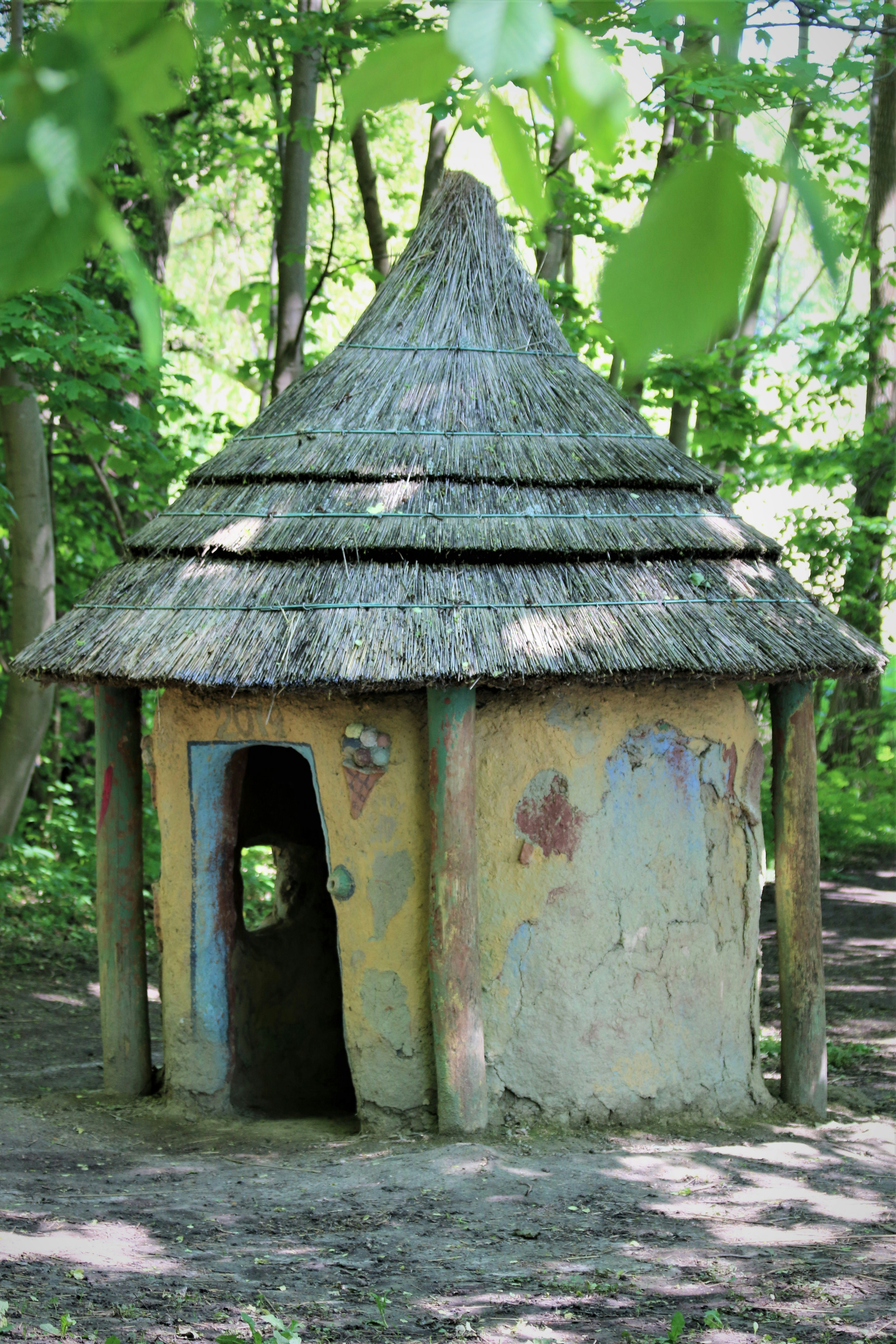A quaint, small hut with a thatched roof nestled among lush green trees, showcasing colorful, weathered walls.