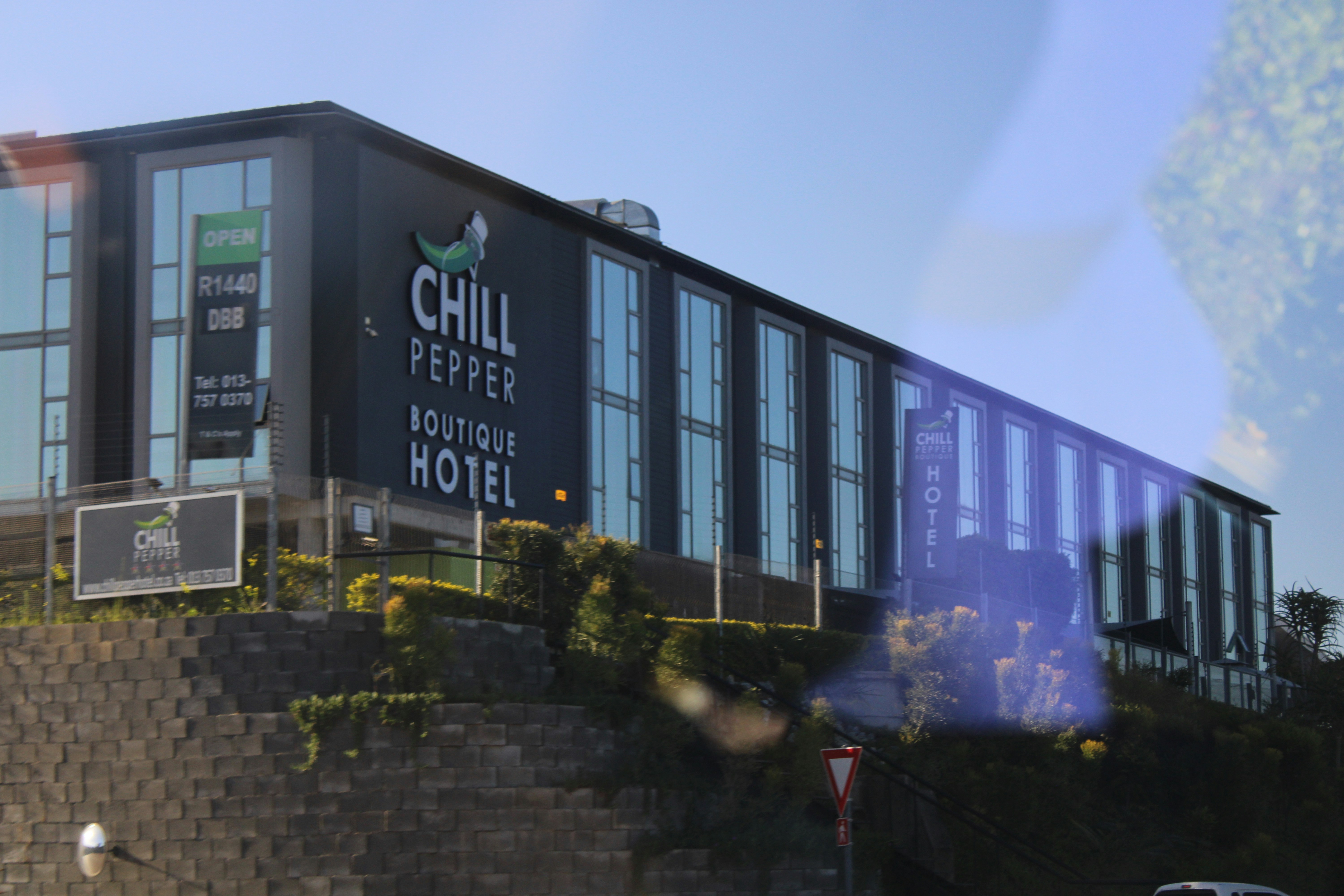 Contemporary hotel facade with reflective windows and lush greenery under a clear blue sky.