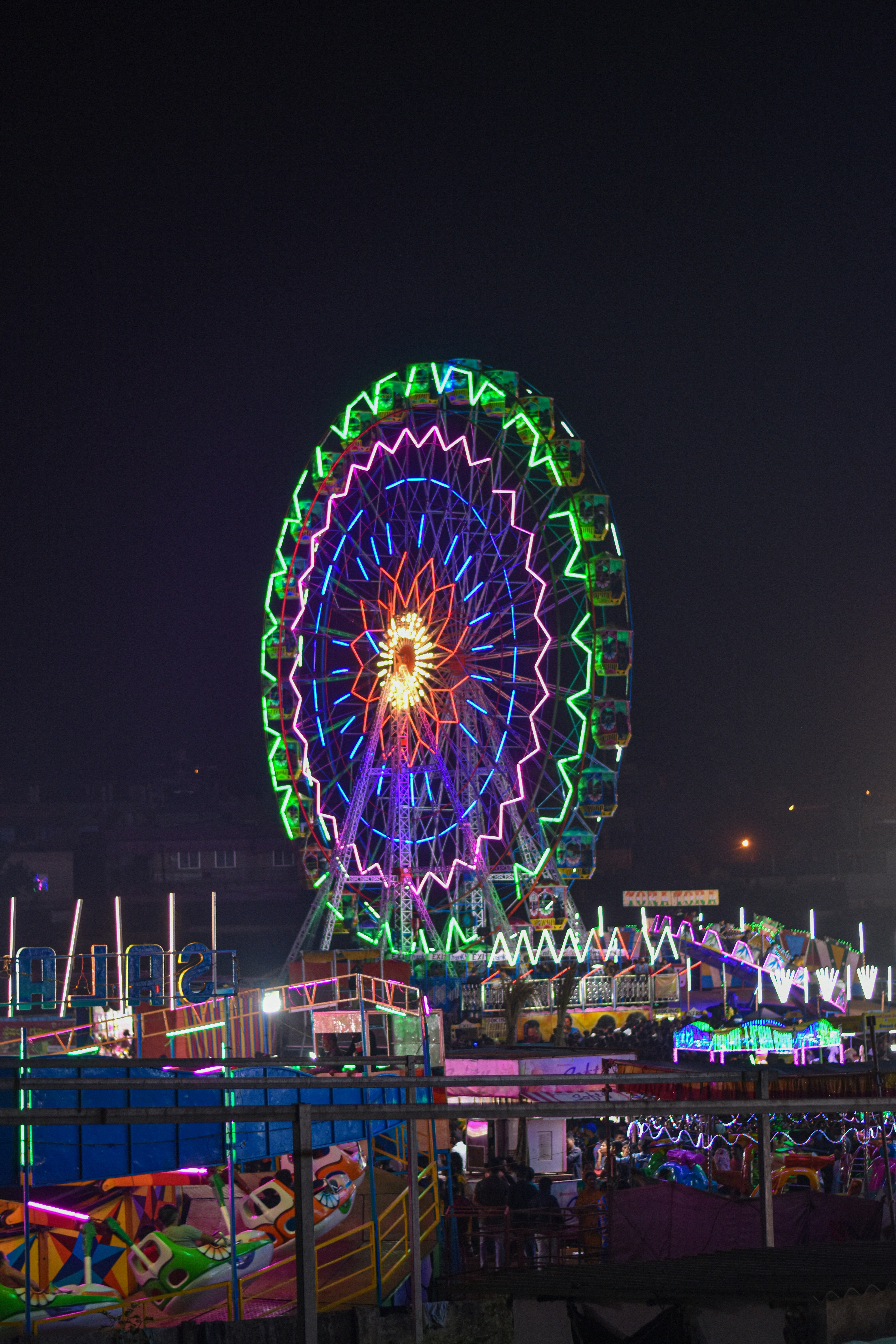 Vibrant Ferris wheel illuminated with colorful lights, surrounded by festive attractions at night.
