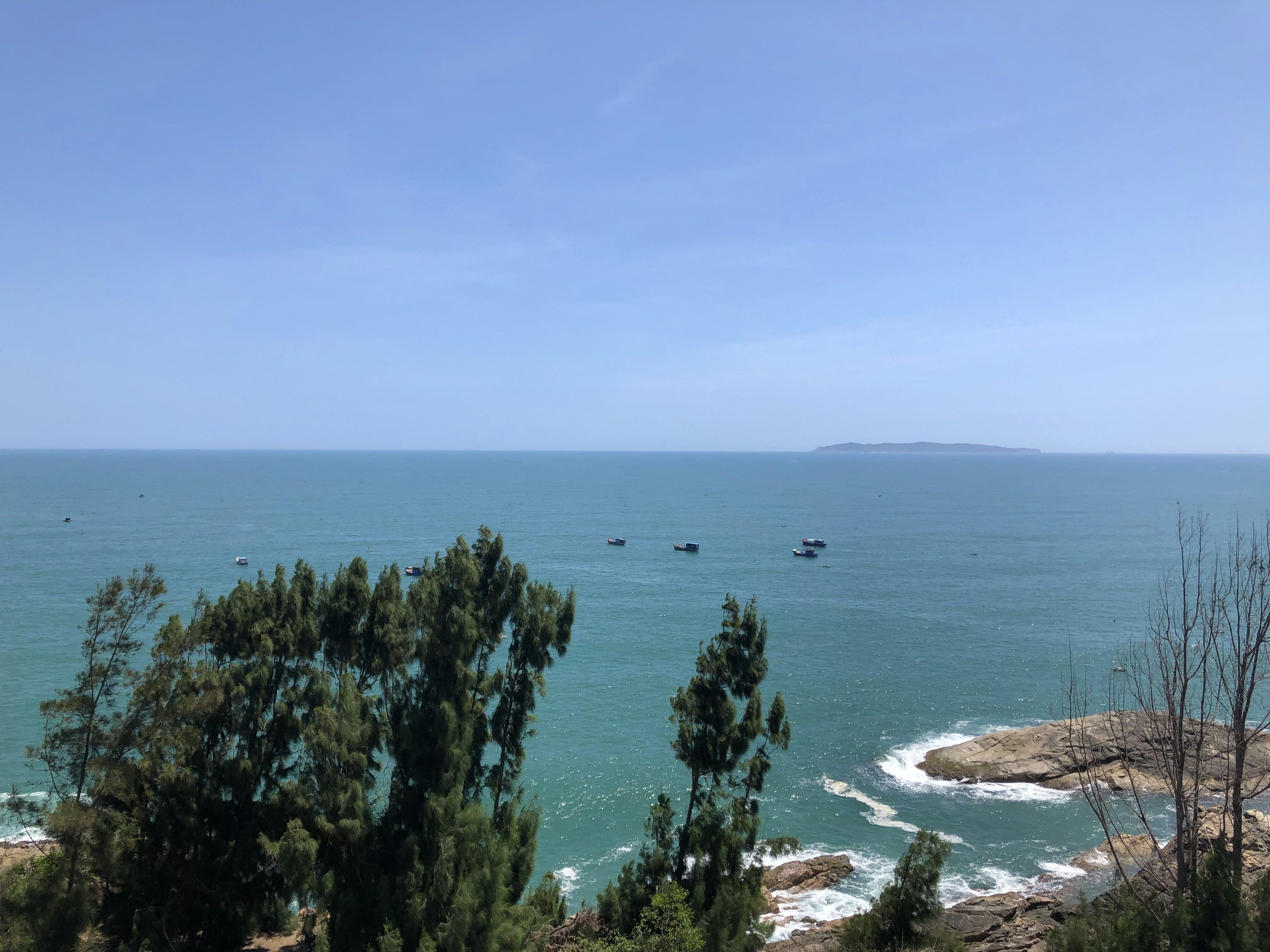 Coastal landscape with turquoise waters and scattered boats under a clear blue sky.