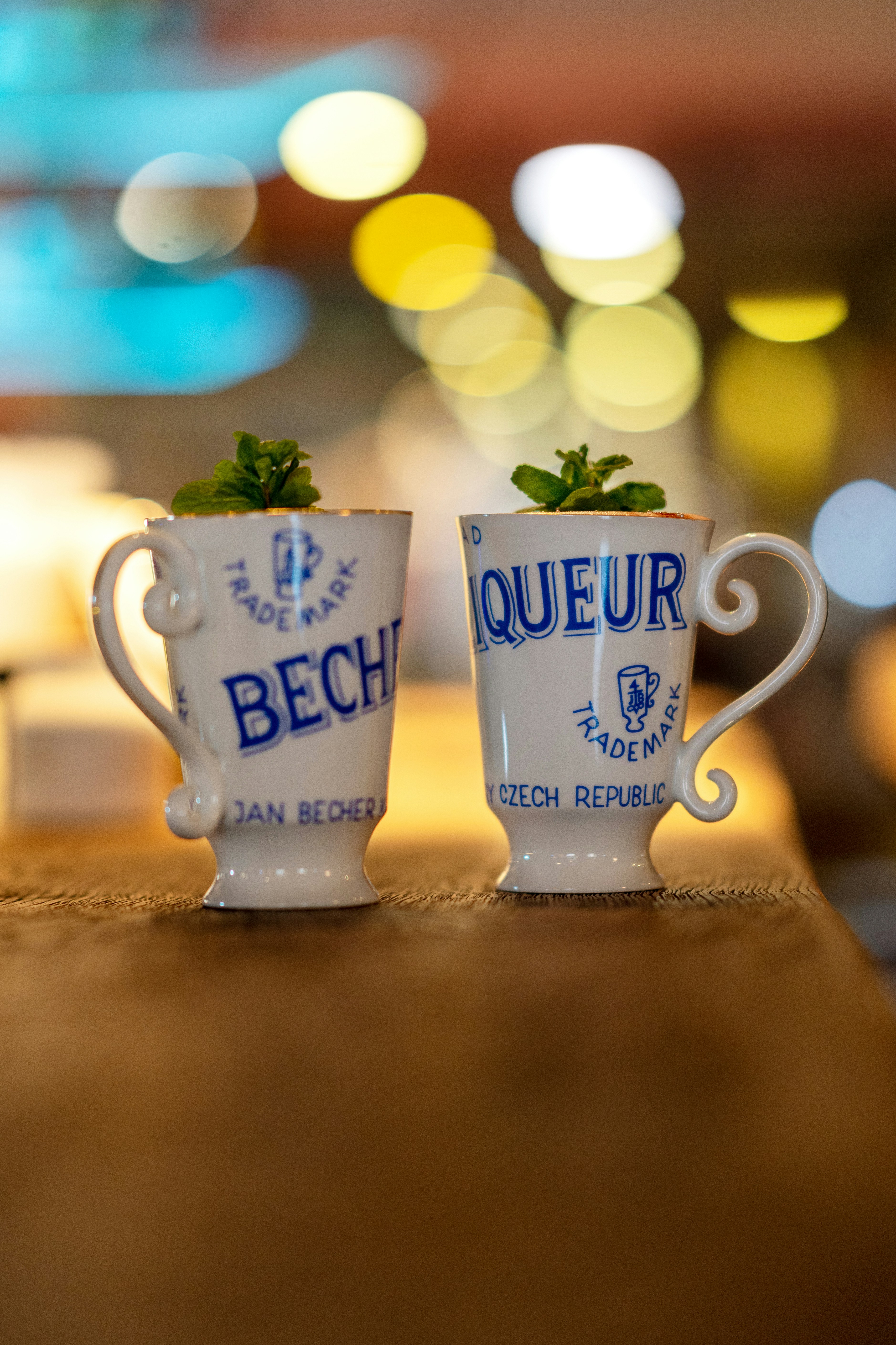 Two blue Becher mugs with mint sprigs on a wooden bar create a cozy bokeh scene
