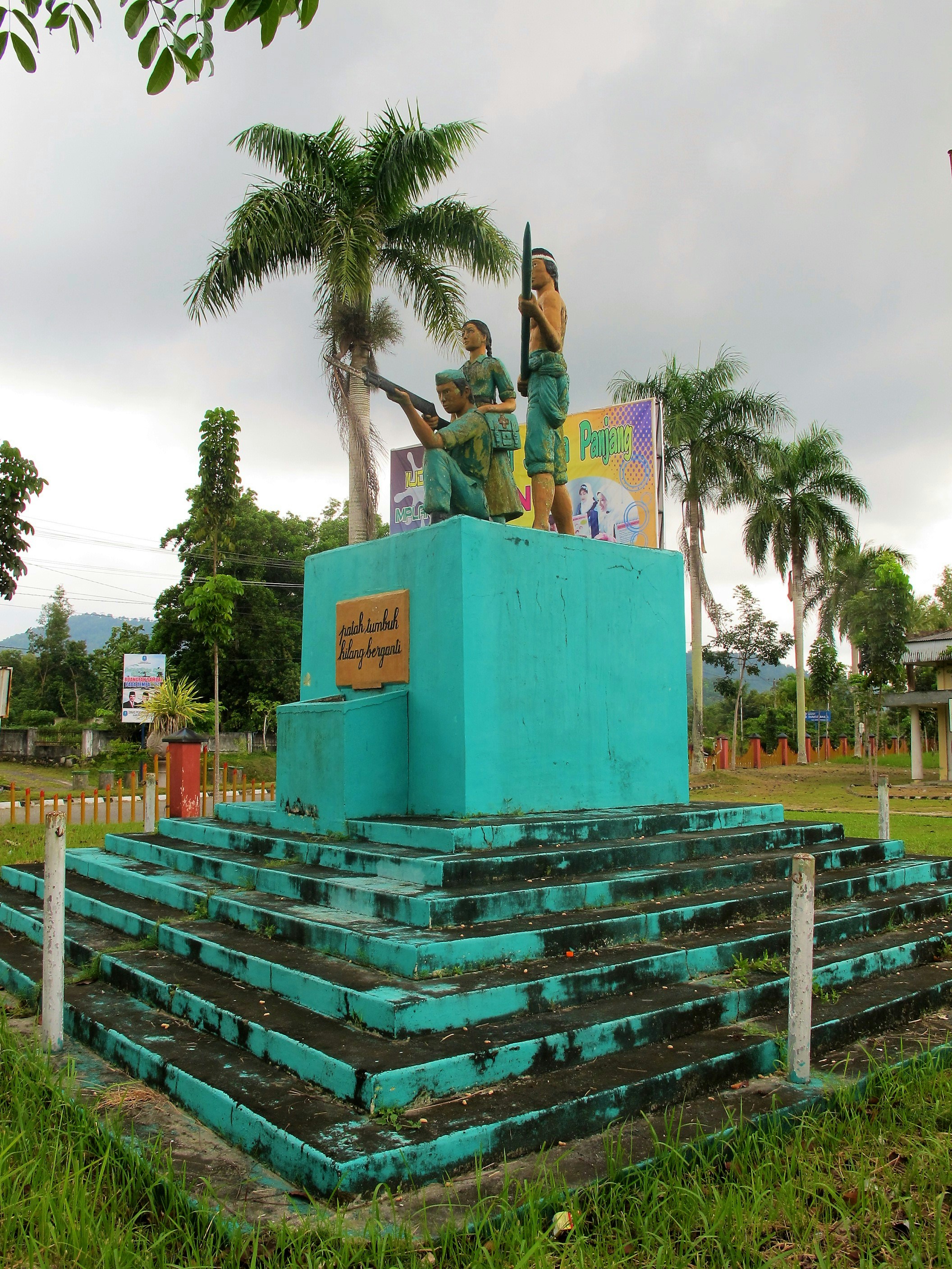 A vibrant turquoise monument featuring three figures, set against a backdrop of palm trees and cloudy skies, celebrating local culture and history.