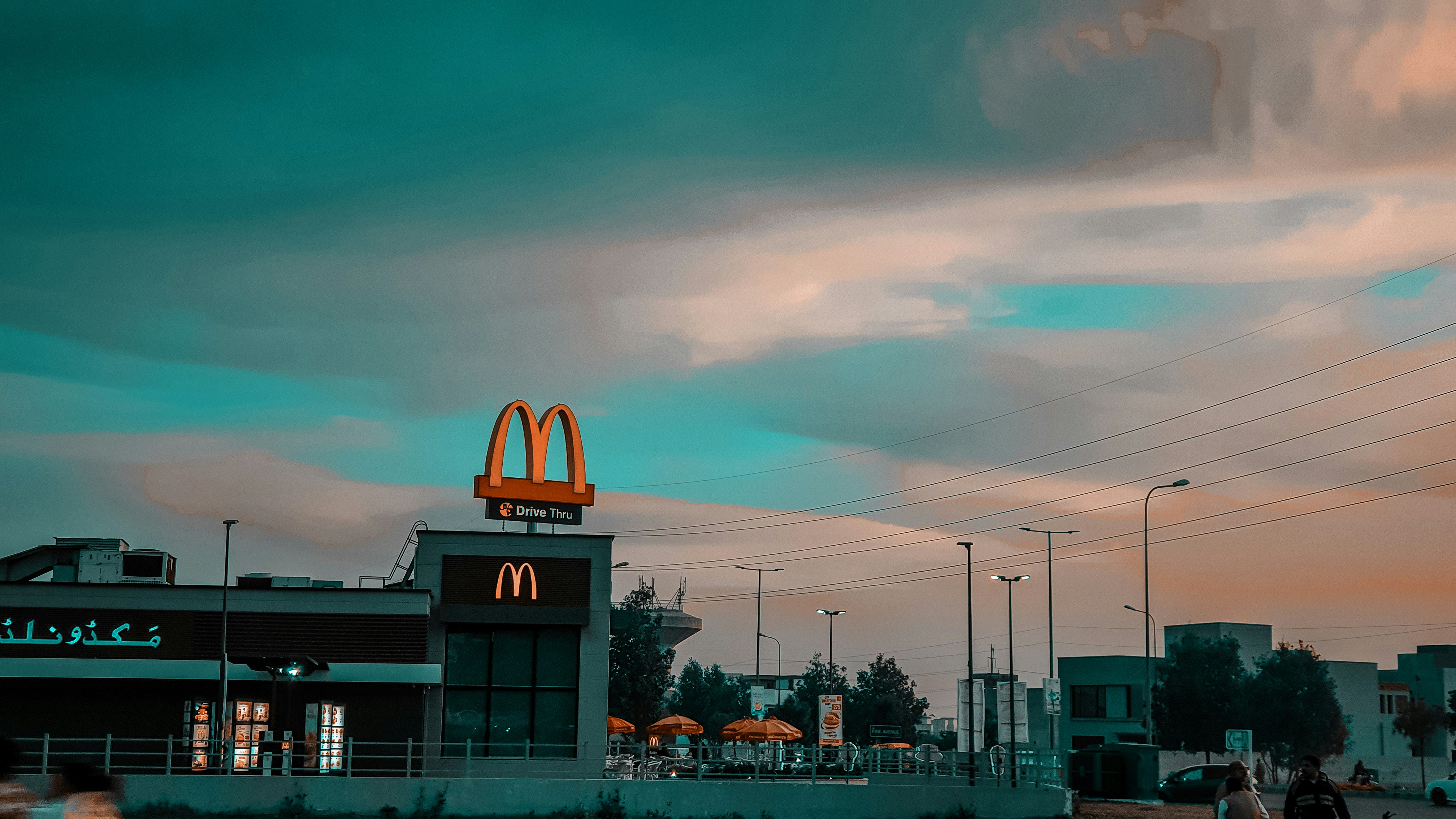 McDonald's restaurant illuminated by a vibrant sunset, with a striking turquoise sky and modern architecture.