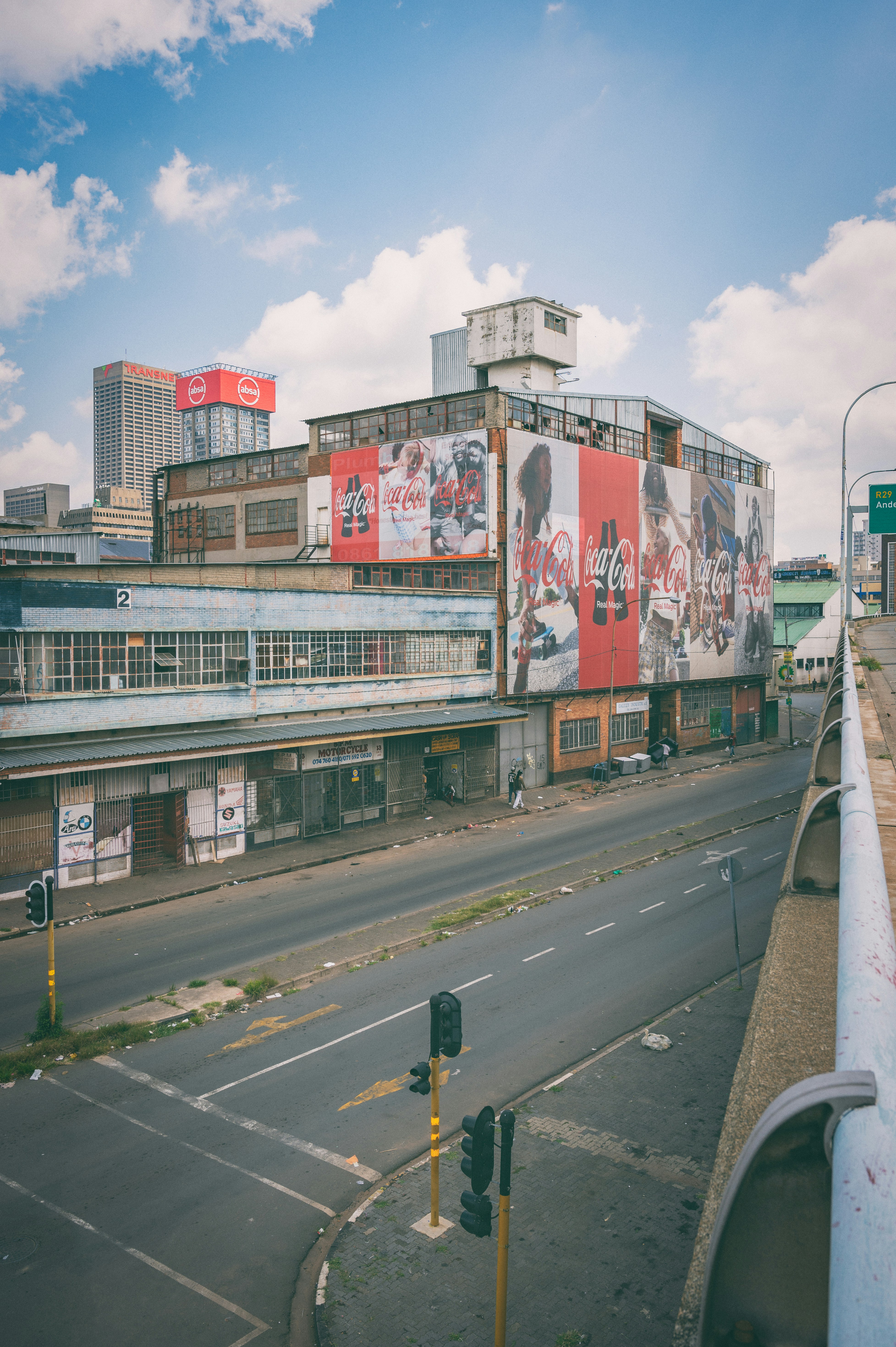 Vibrant Coca-Cola mural adorning an industrial building, with a backdrop of city skyscrapers under a cloudy sky.